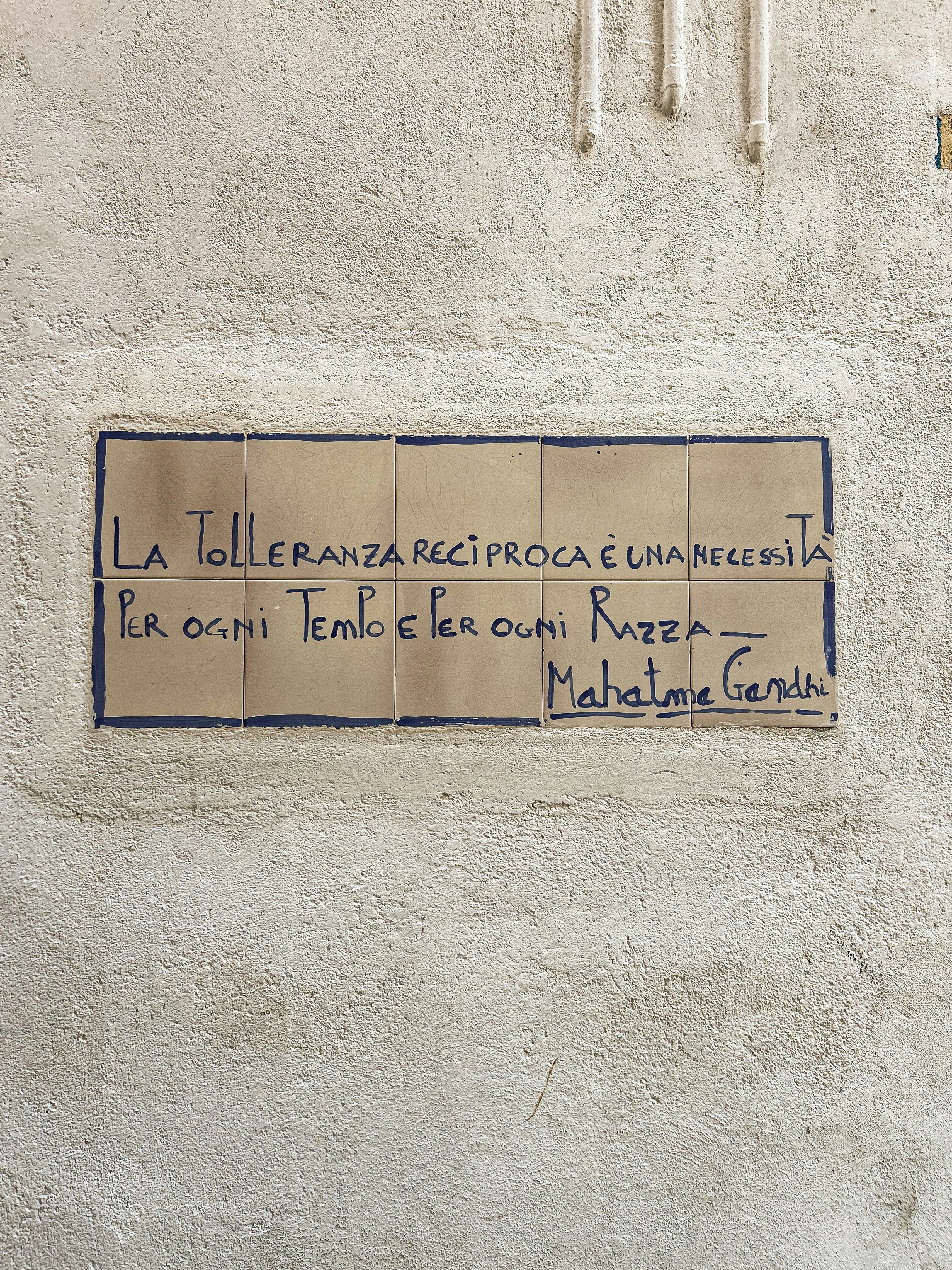 A handwritten quote by Gandhi painted on ceramic tiles brings a message of mutual tolerance. A simple, powerful reminder set against the quiet texture of a Sicilian wall.