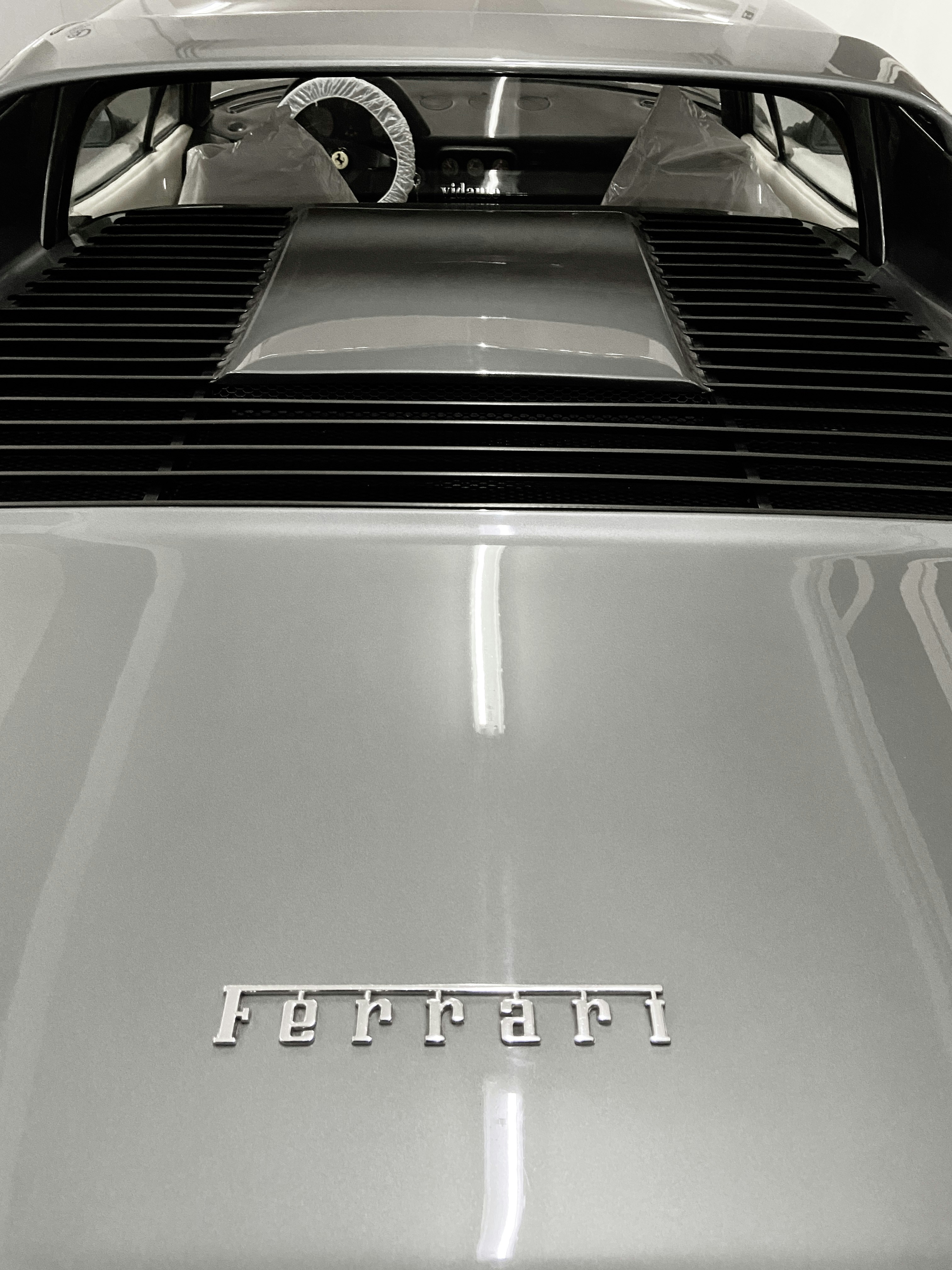 A clean, minimal close-up of the Ferrari emblem on a metallic silver engine cover. Pure precision and automotive perfection.