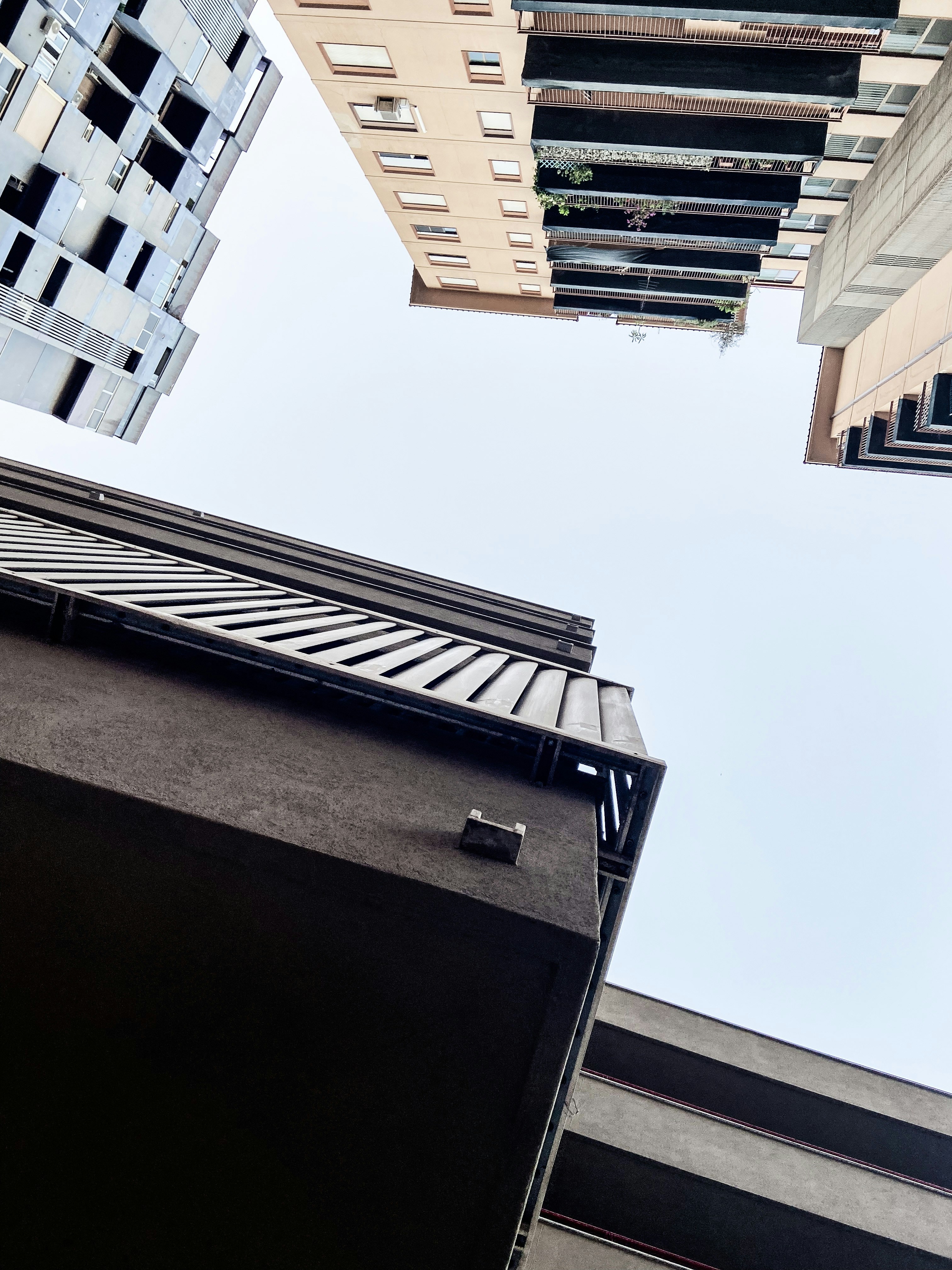 A geometric view of tall buildings captured from below, creating a clean frame against the pale sky. Lines, symmetry, and urban minimalism.