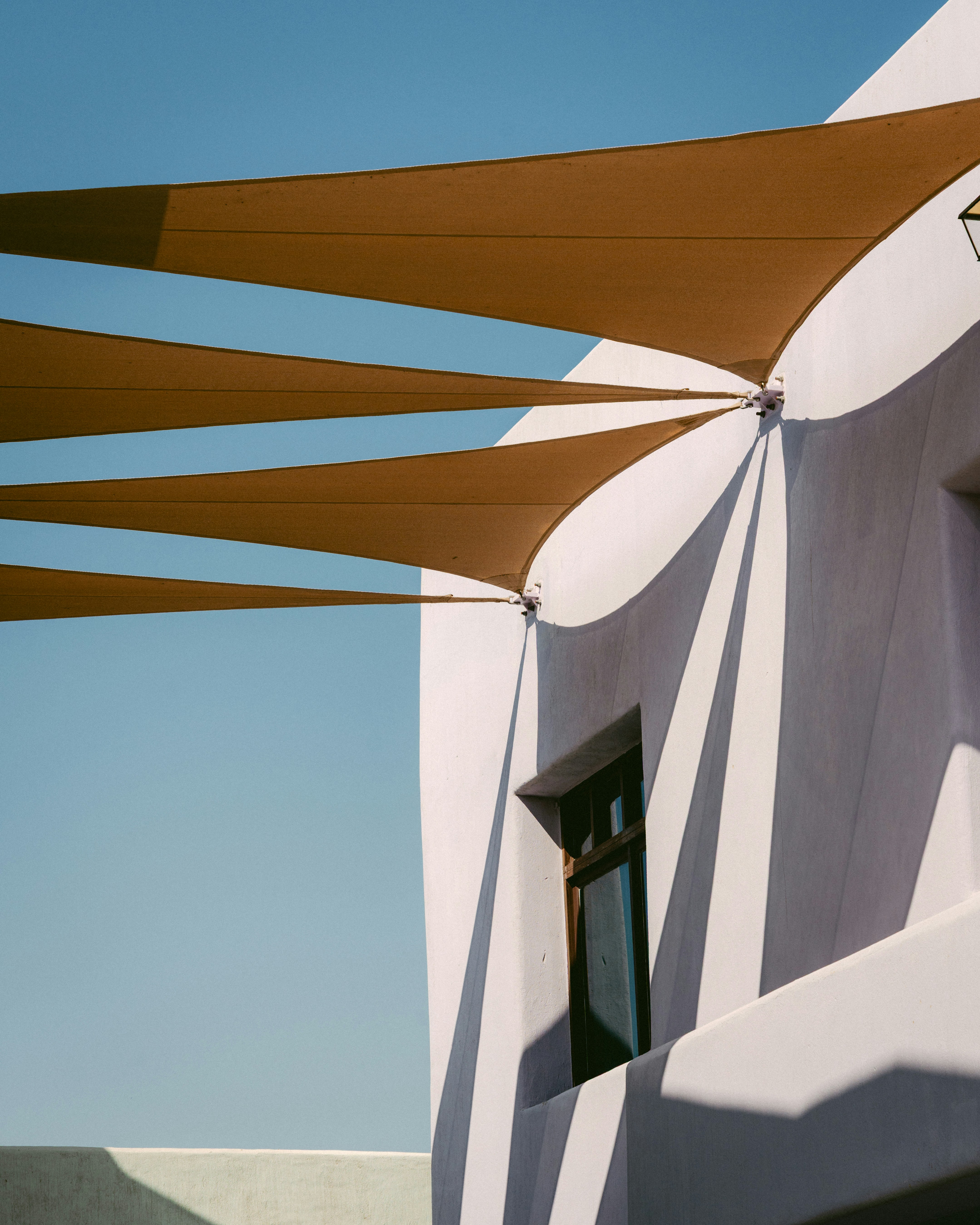 Tan shade sails casting shadows on a white building. photo – Free ...