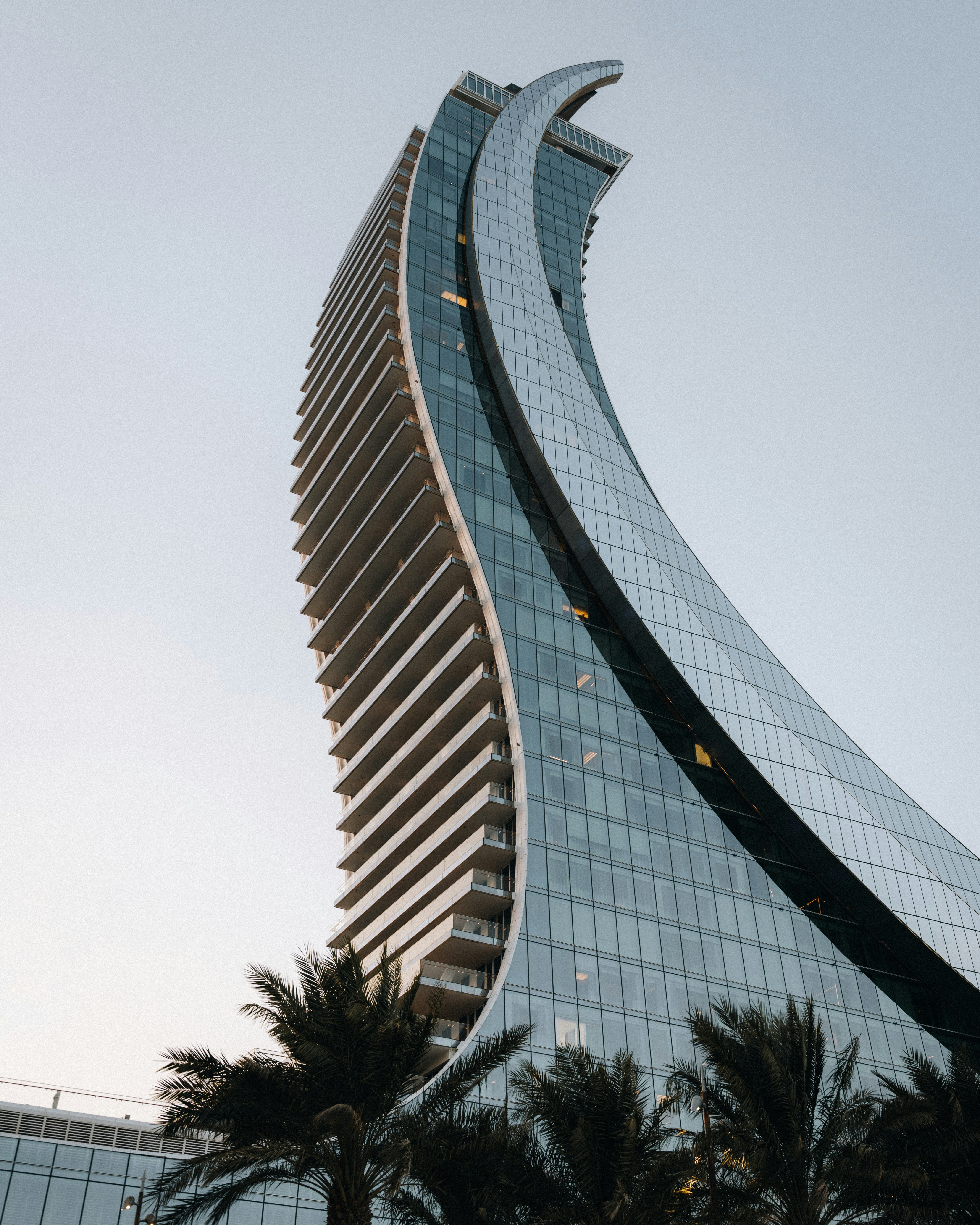 Arc of Glass: The Crescent Tower Rises Over Palm Canopy