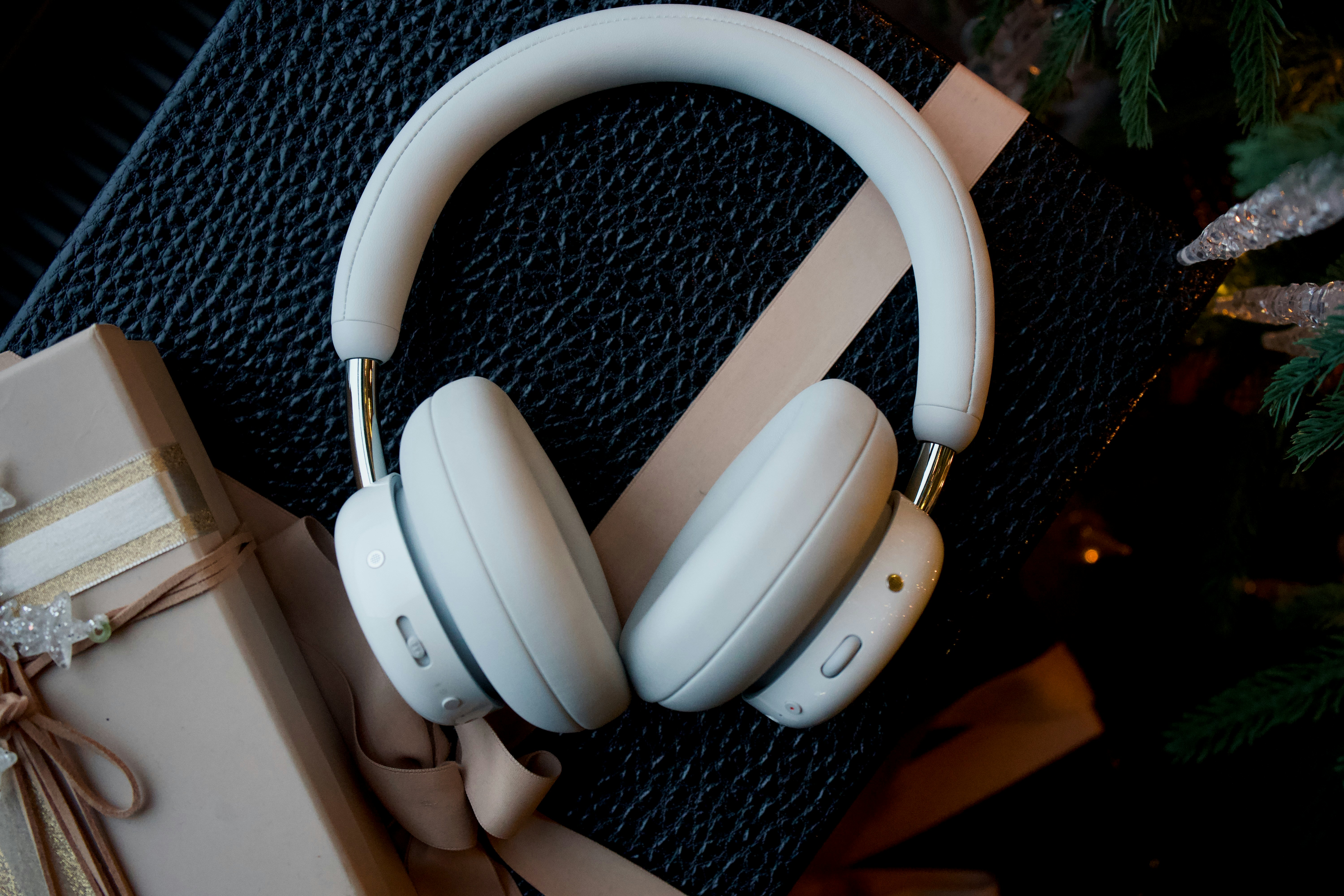 Ivory over-ear headphones cradled by gift-wrap under festive greens.