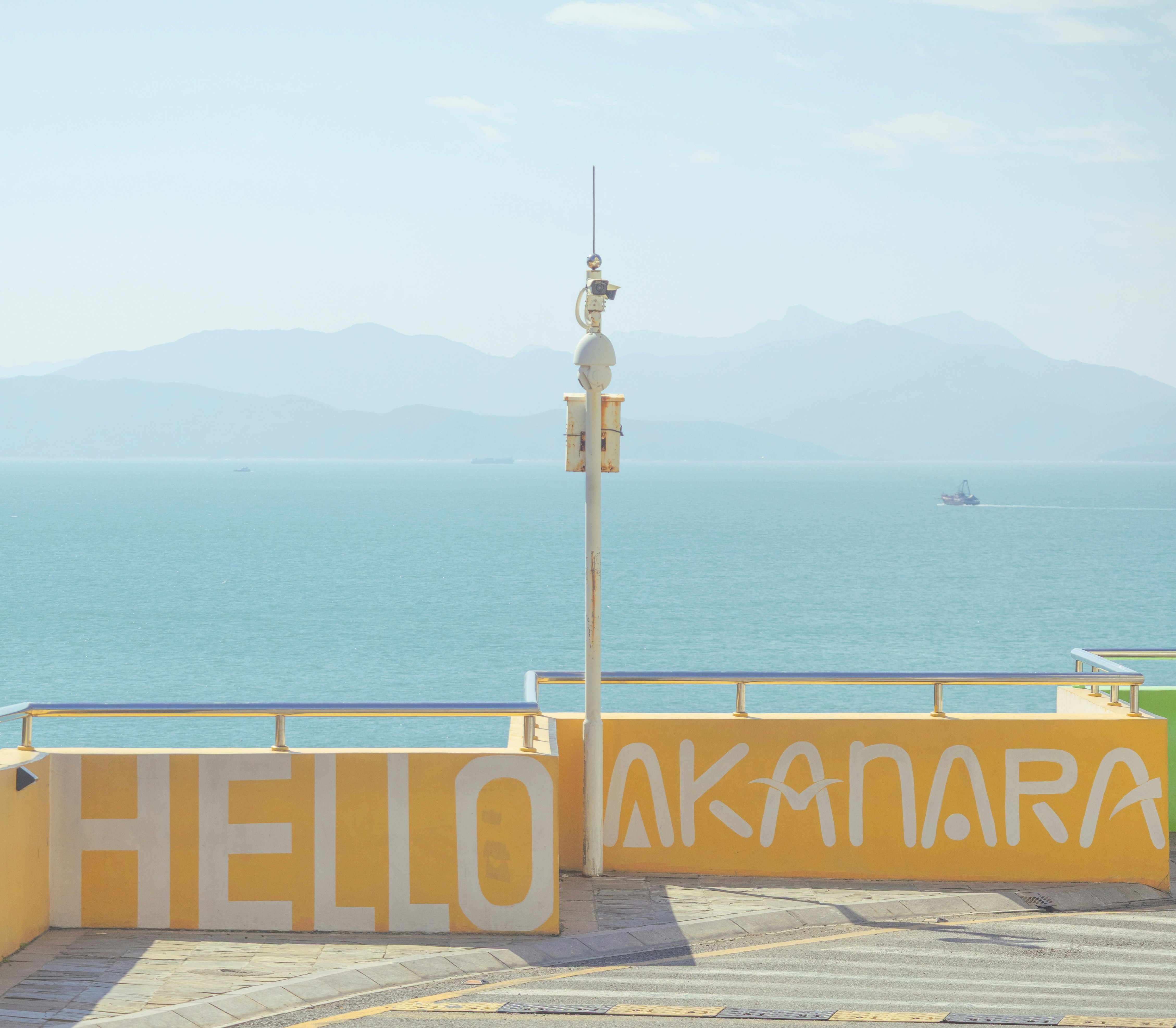 Pole-top Sentinel over a sunlit Hello wall: a minimalist coastal scene