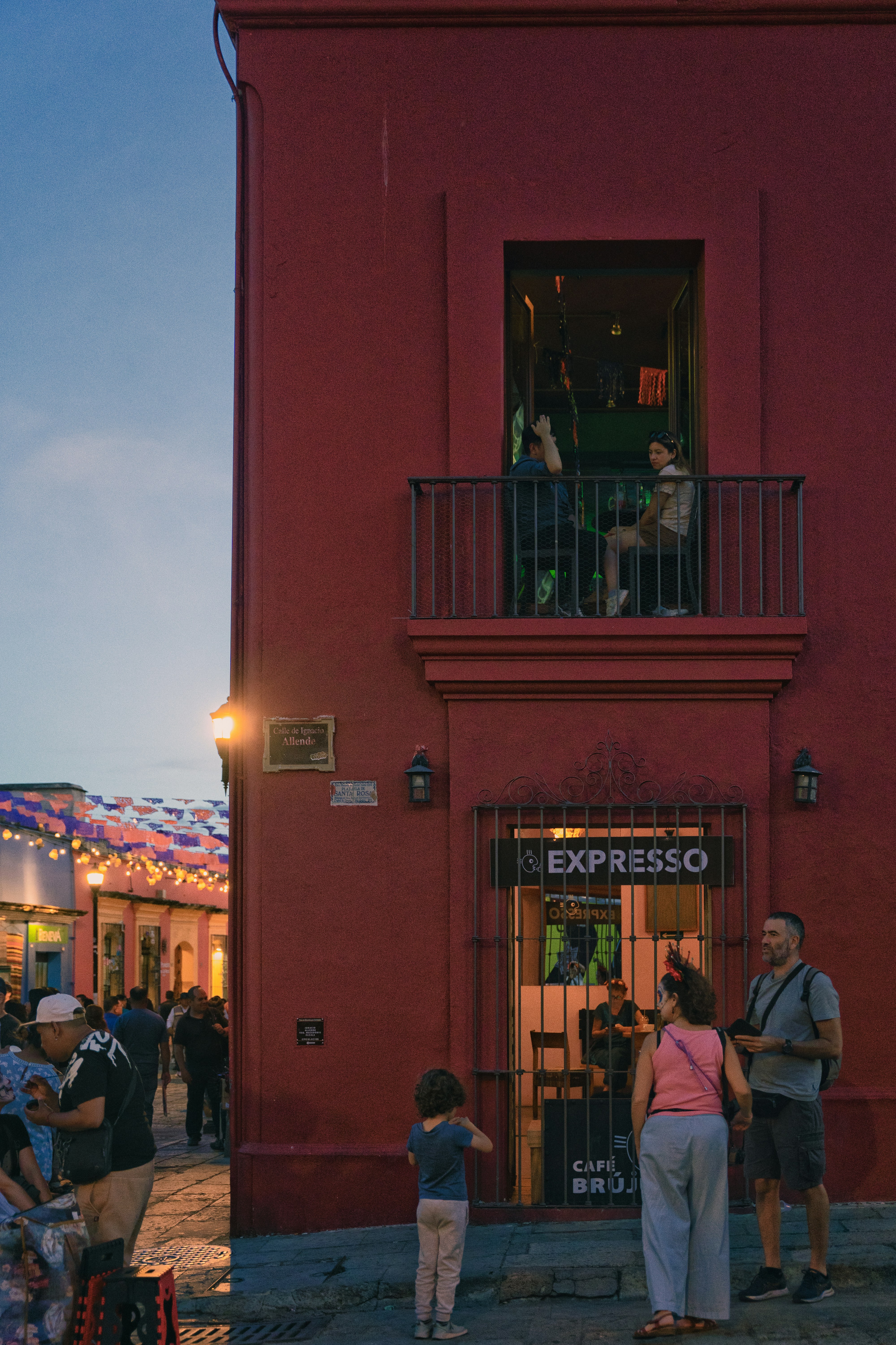 Crimson Balcony at Dusk: Quiet Pause Above a Lively Espresso Café