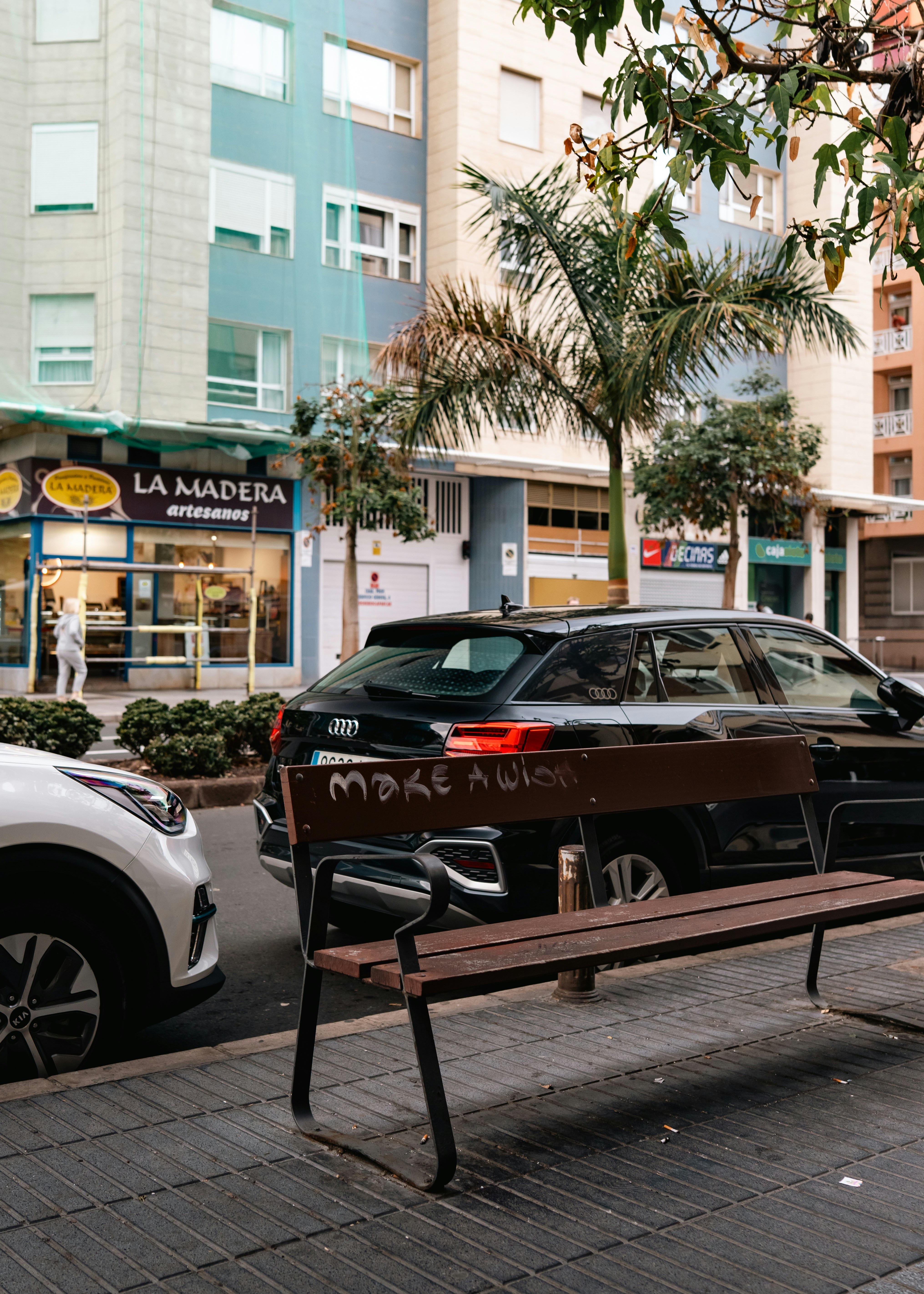 Graffiti-Bench, Palm Shadows, and a Glossy SUV on a Sunlit Street