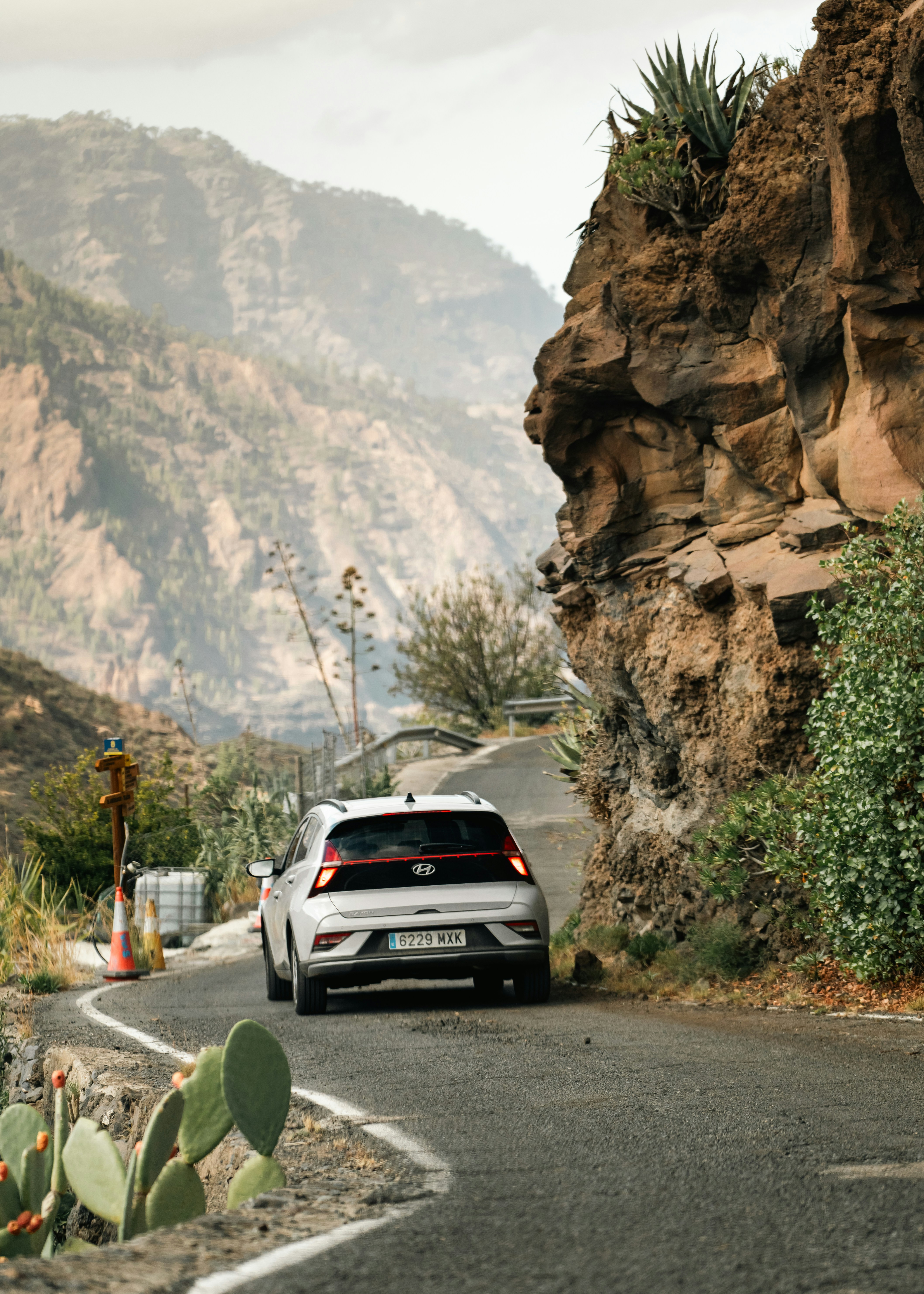 White hatchback on a winding cliffside road framed by rugged rock formations