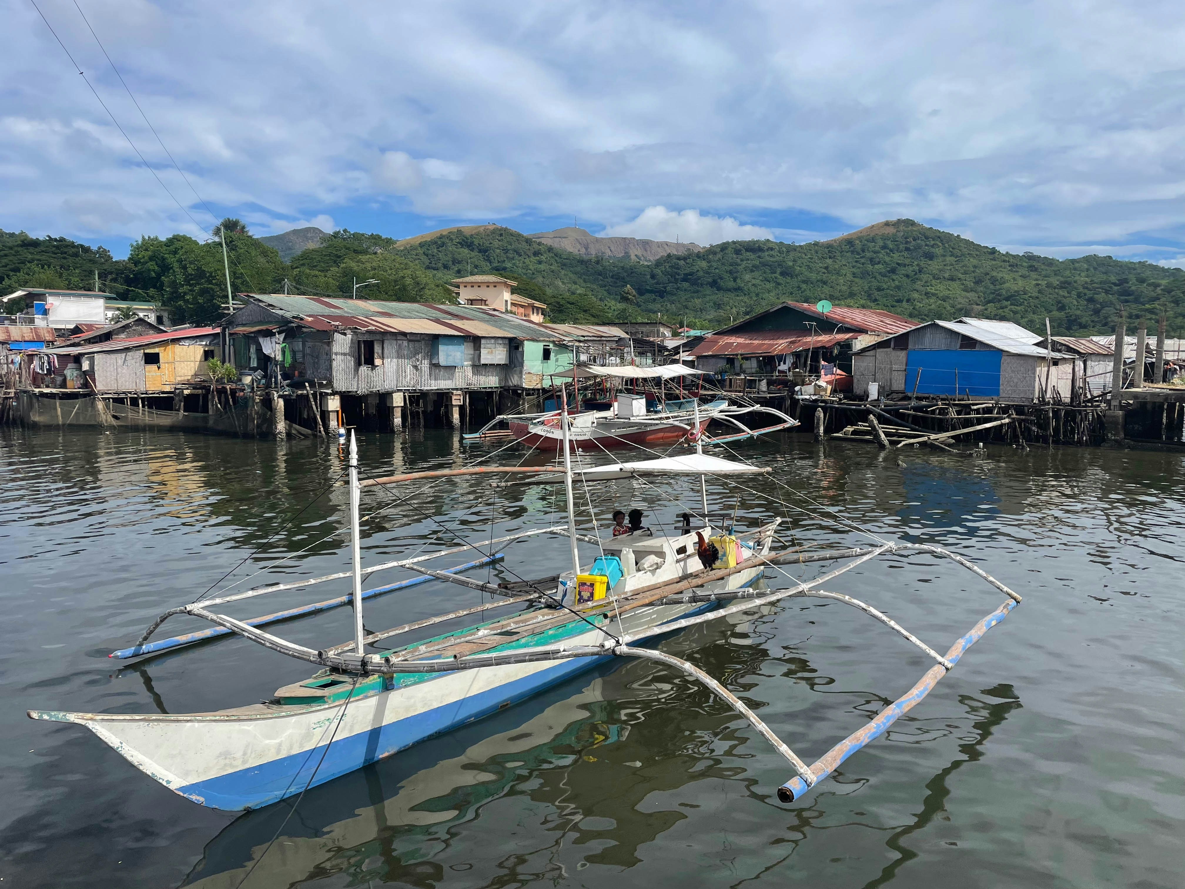A traditional outrigger boat floats near stilt houses. photo – Free ...