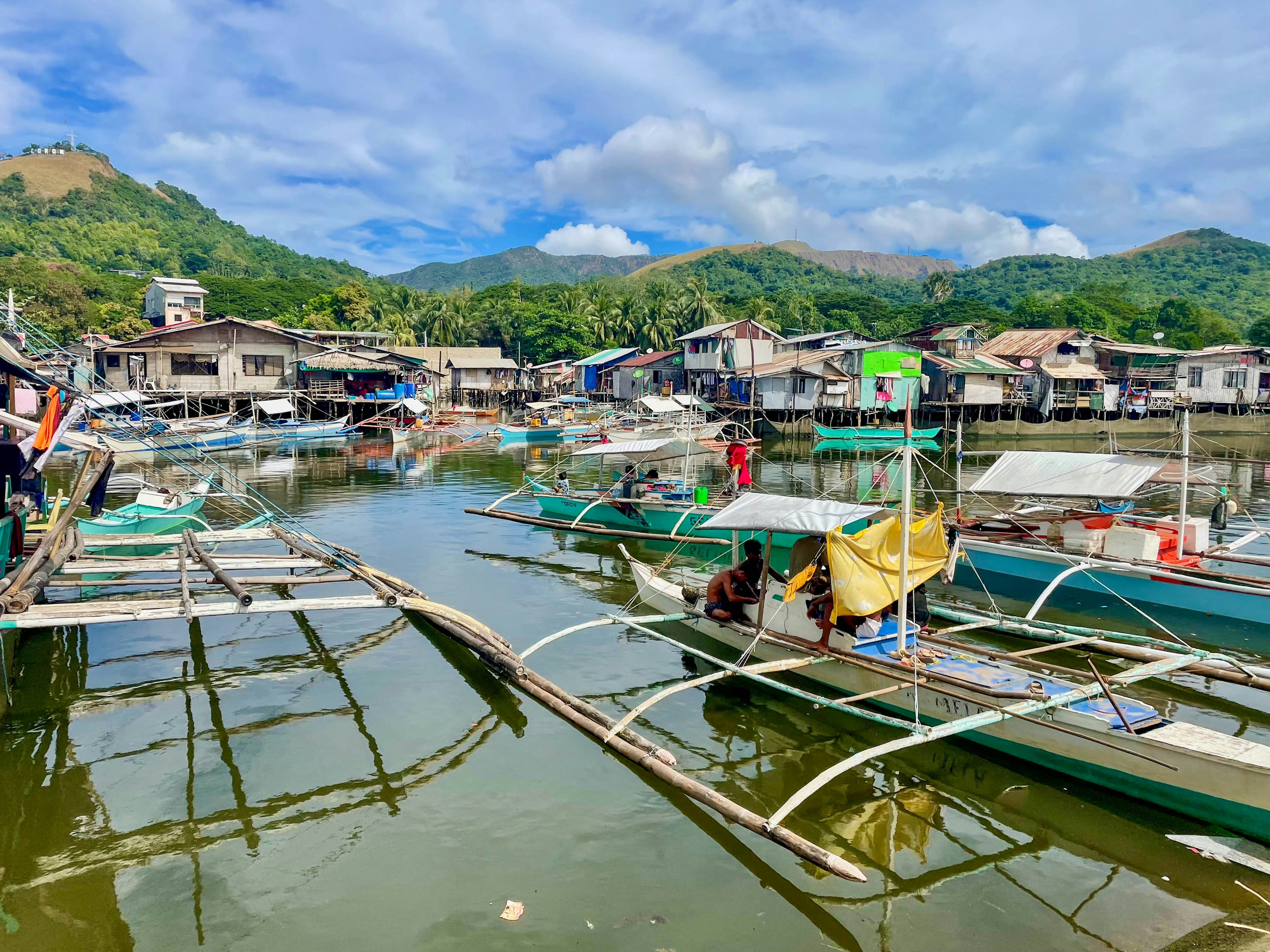 Stilt-House Harbor: Boats Lined Along a Calm Lagoon Beneath Green Hills