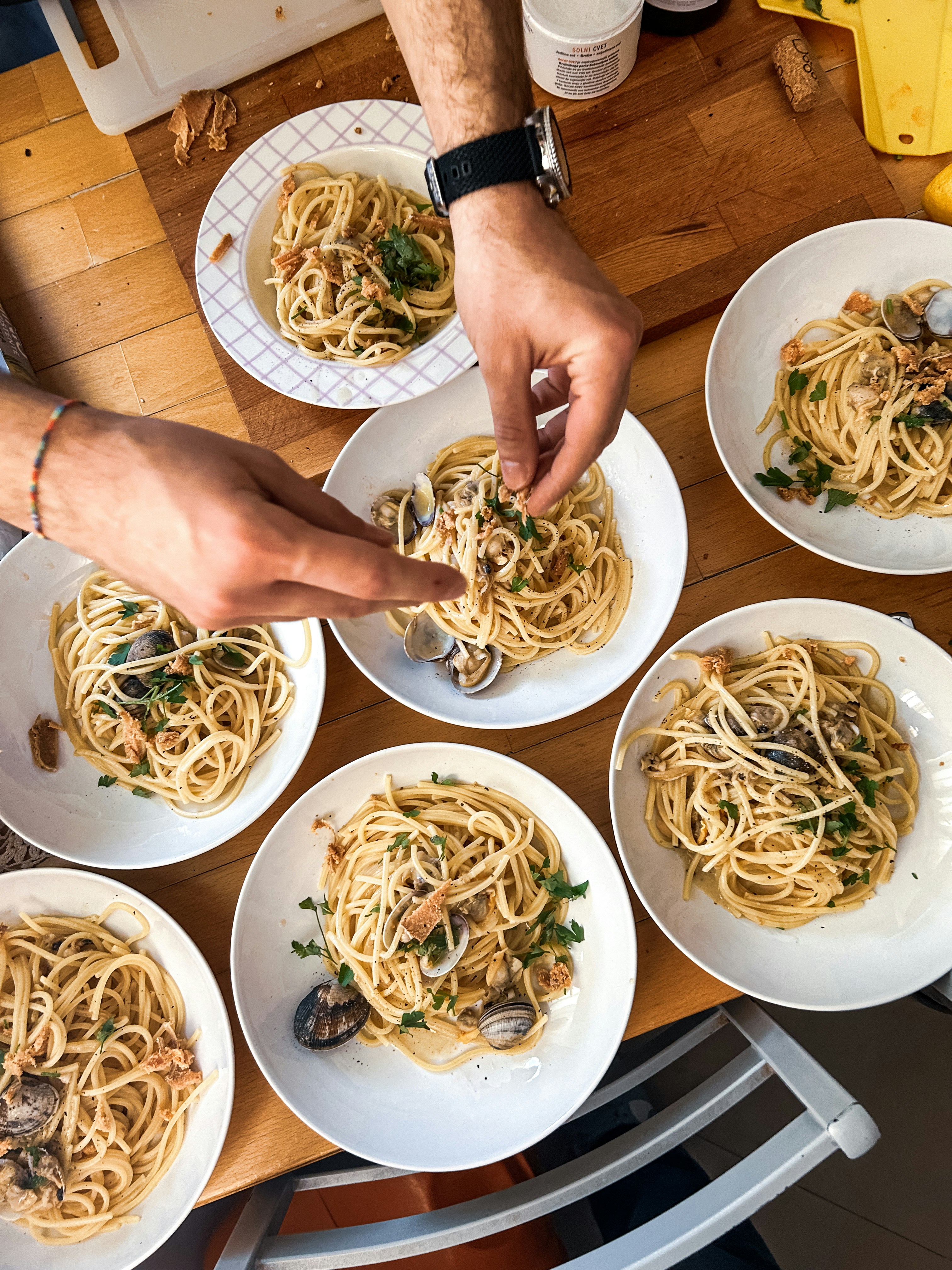 Hands garnishing plates of spaghetti with clams