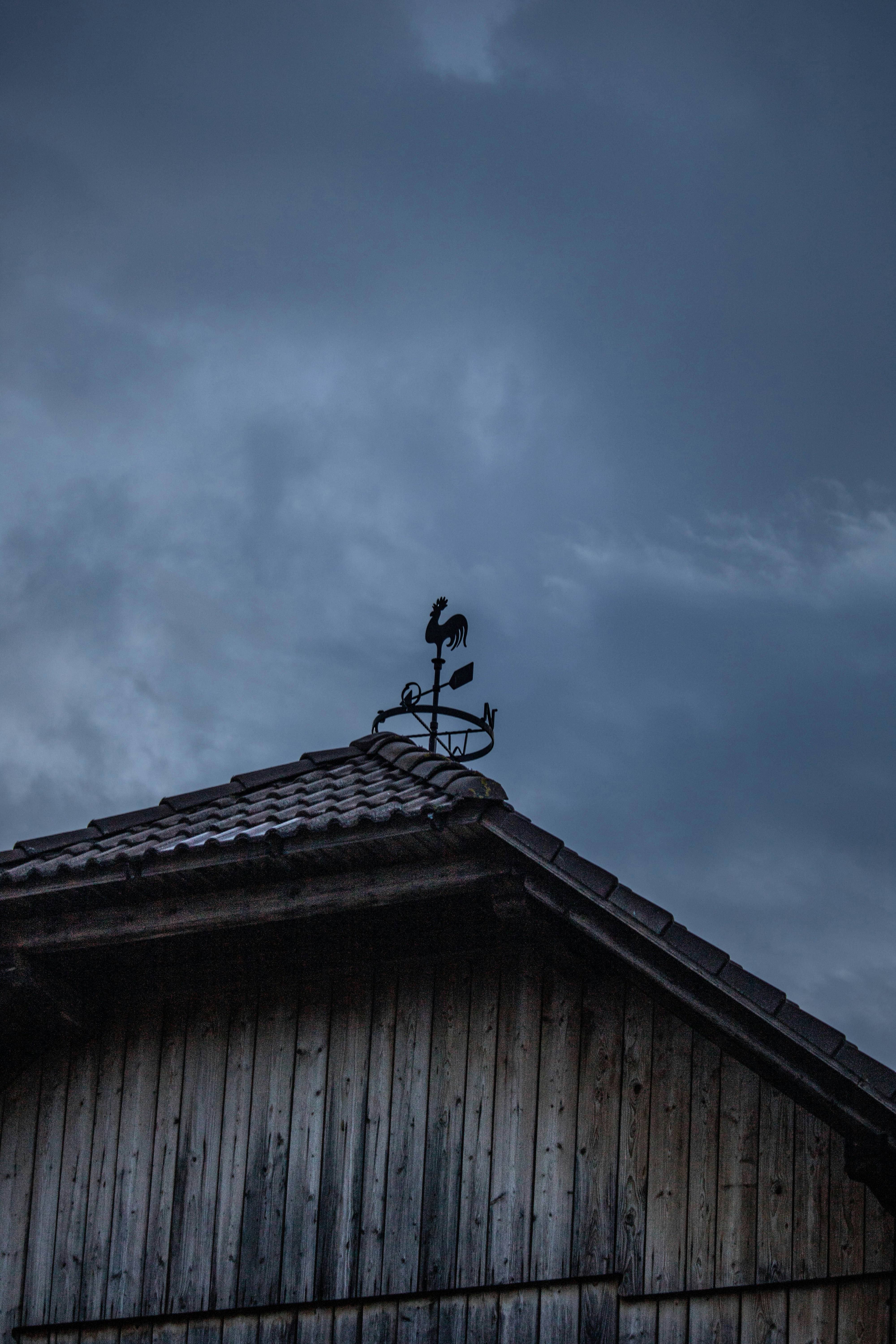 Rooster Weathervane Stands Sentinel Over a Weathered Roof at Dusk