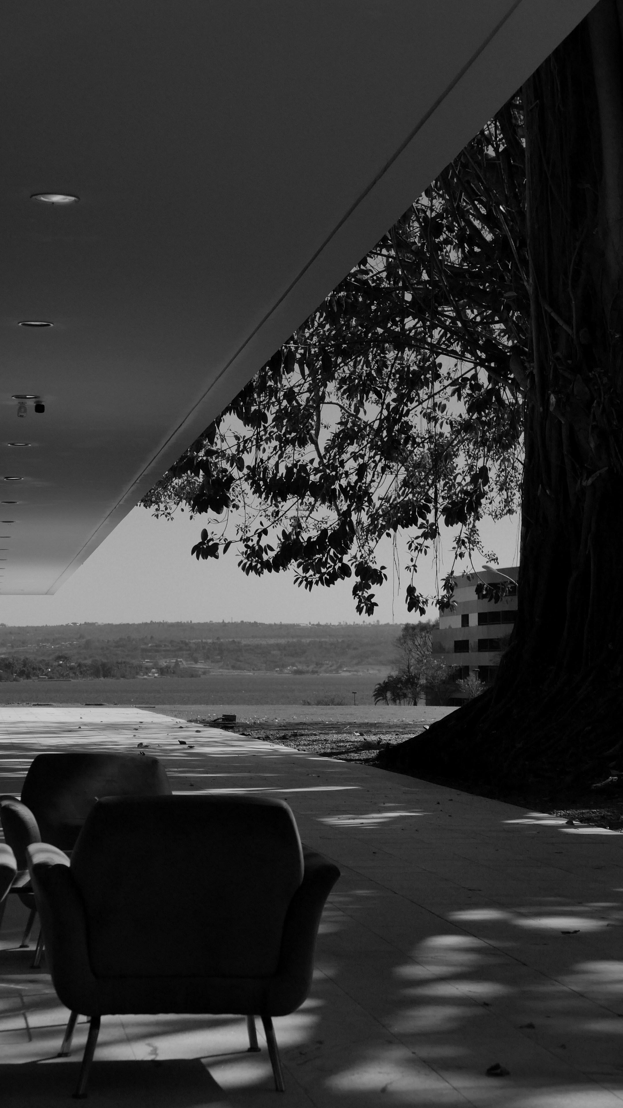 Cantilevered Quiet: Chairs Under a Diagonal Shelter Framing a Distant Waterfront