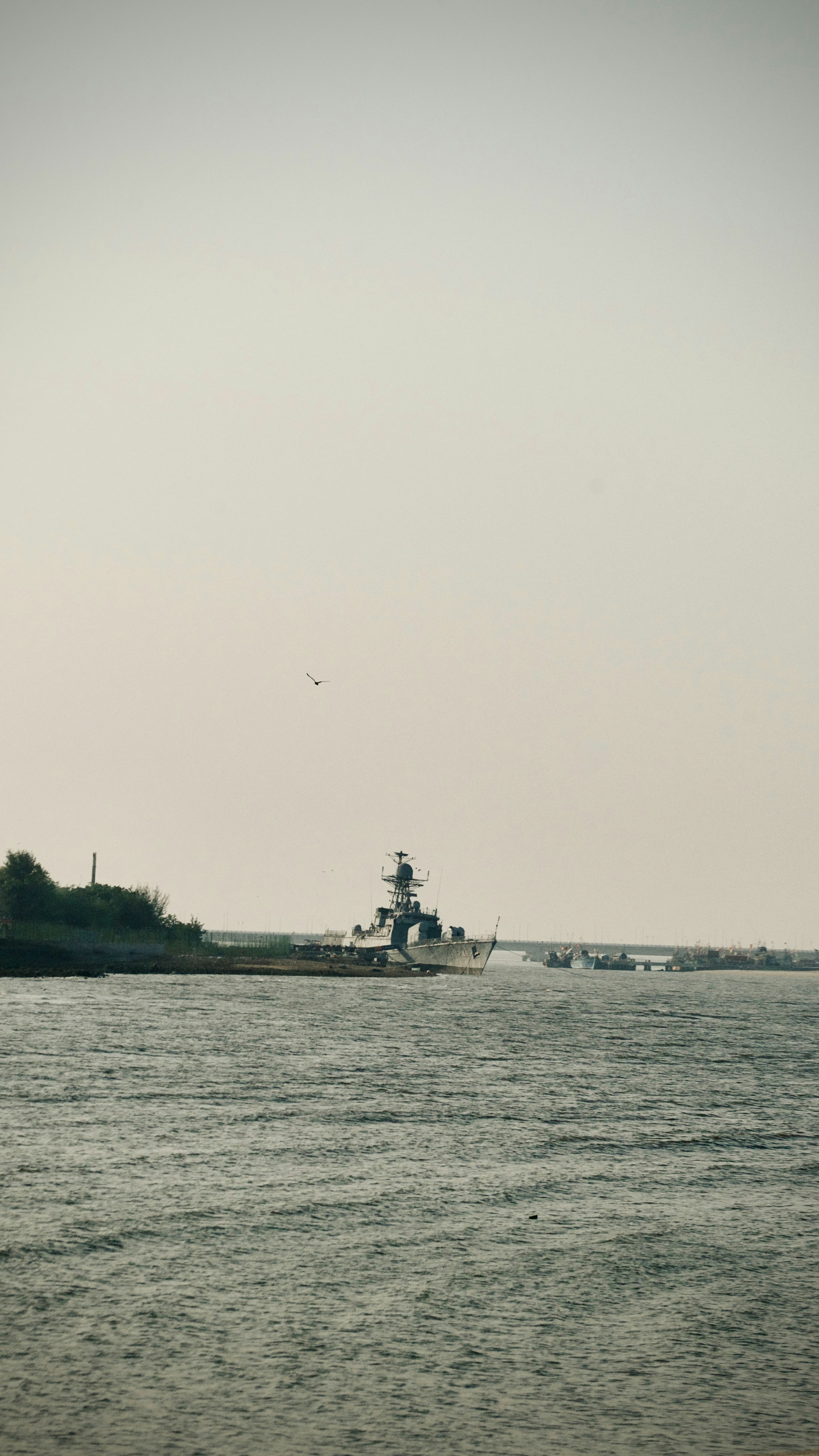 Harbor Sentinel at Dusk: A naval vessel rests along a calm river mouth