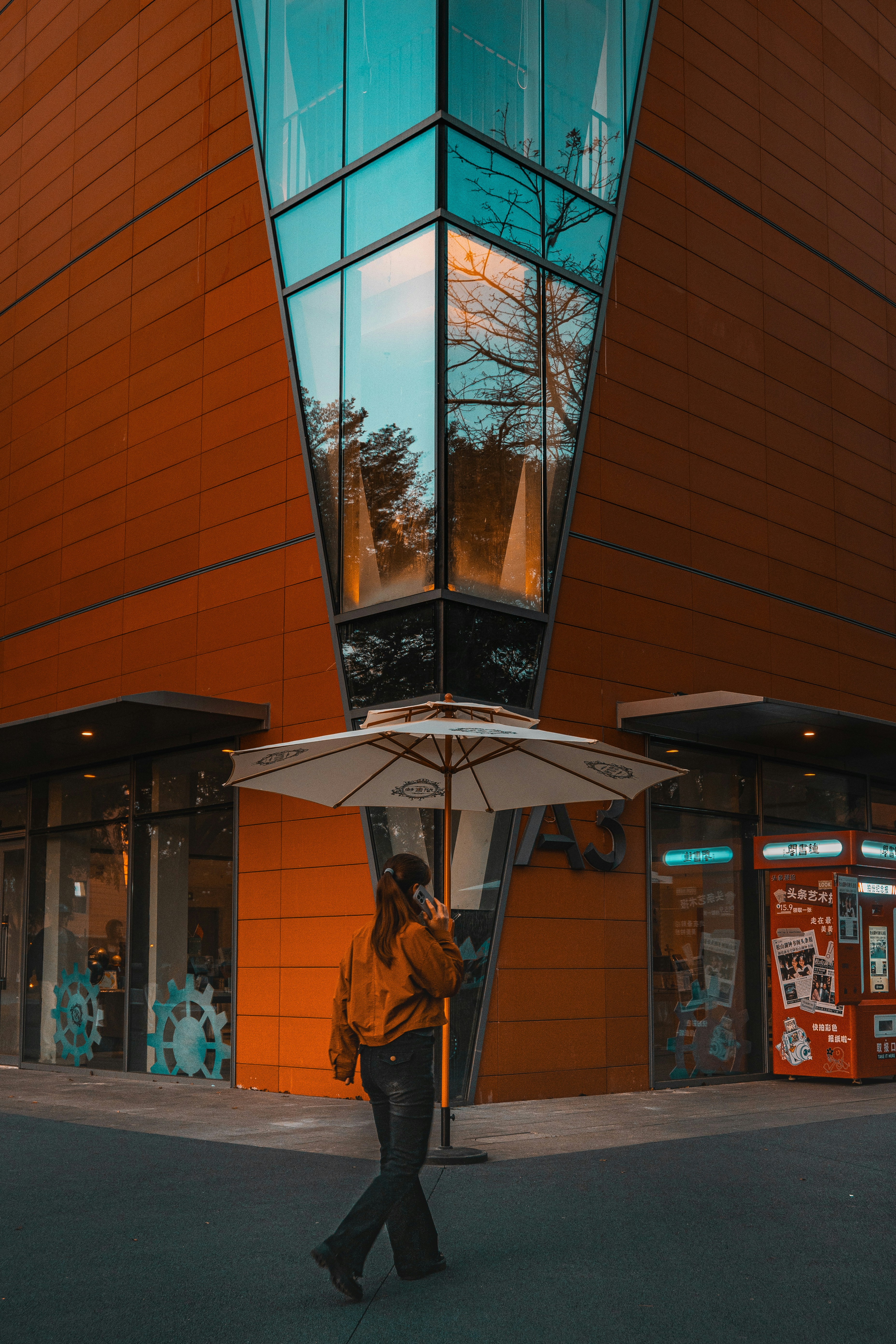 Woman with umbrella walks by modern orange building
