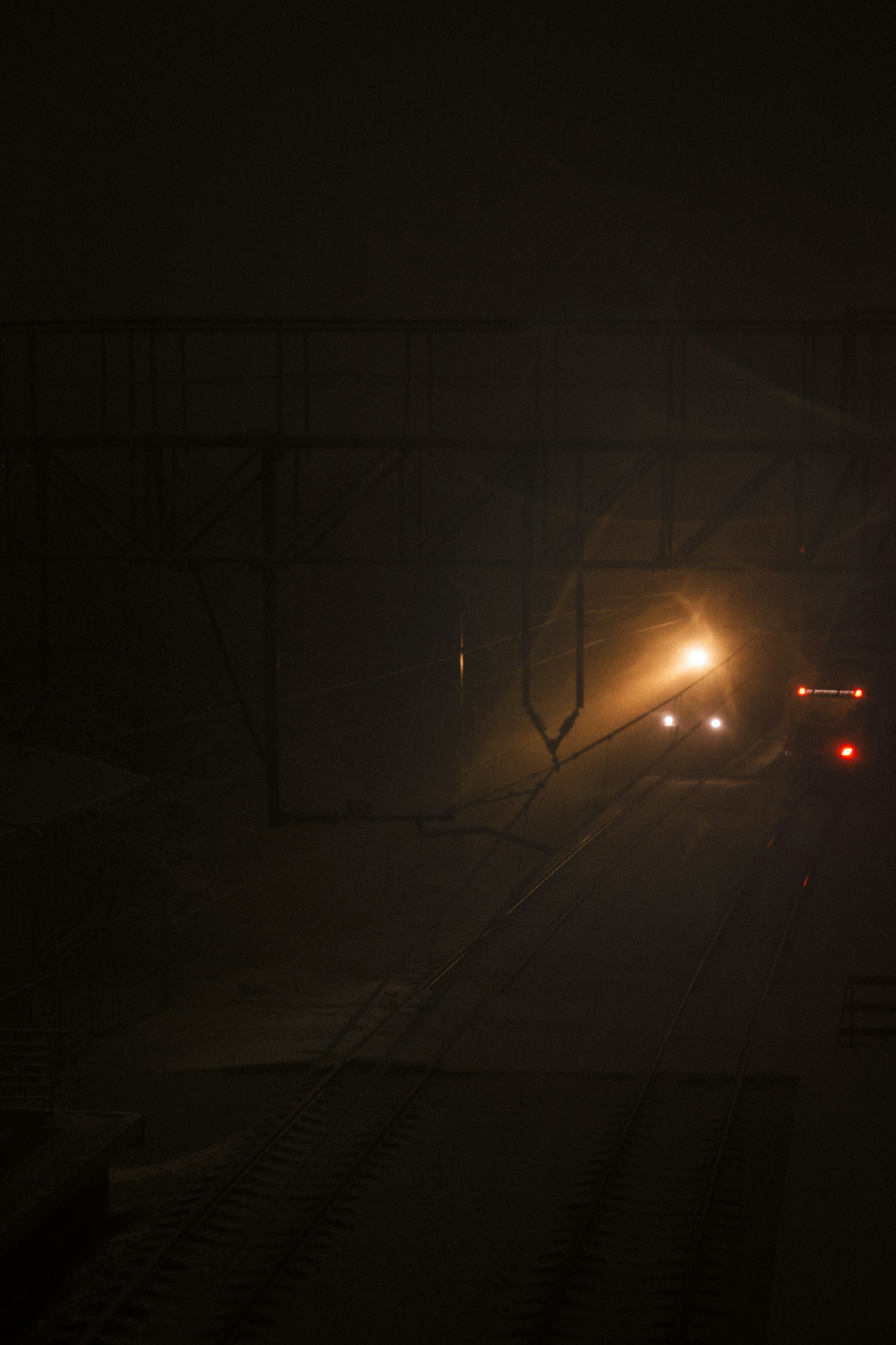 Midnight Approach: Headlights Carve Through Fog Beneath a Quiet Rail Bridge