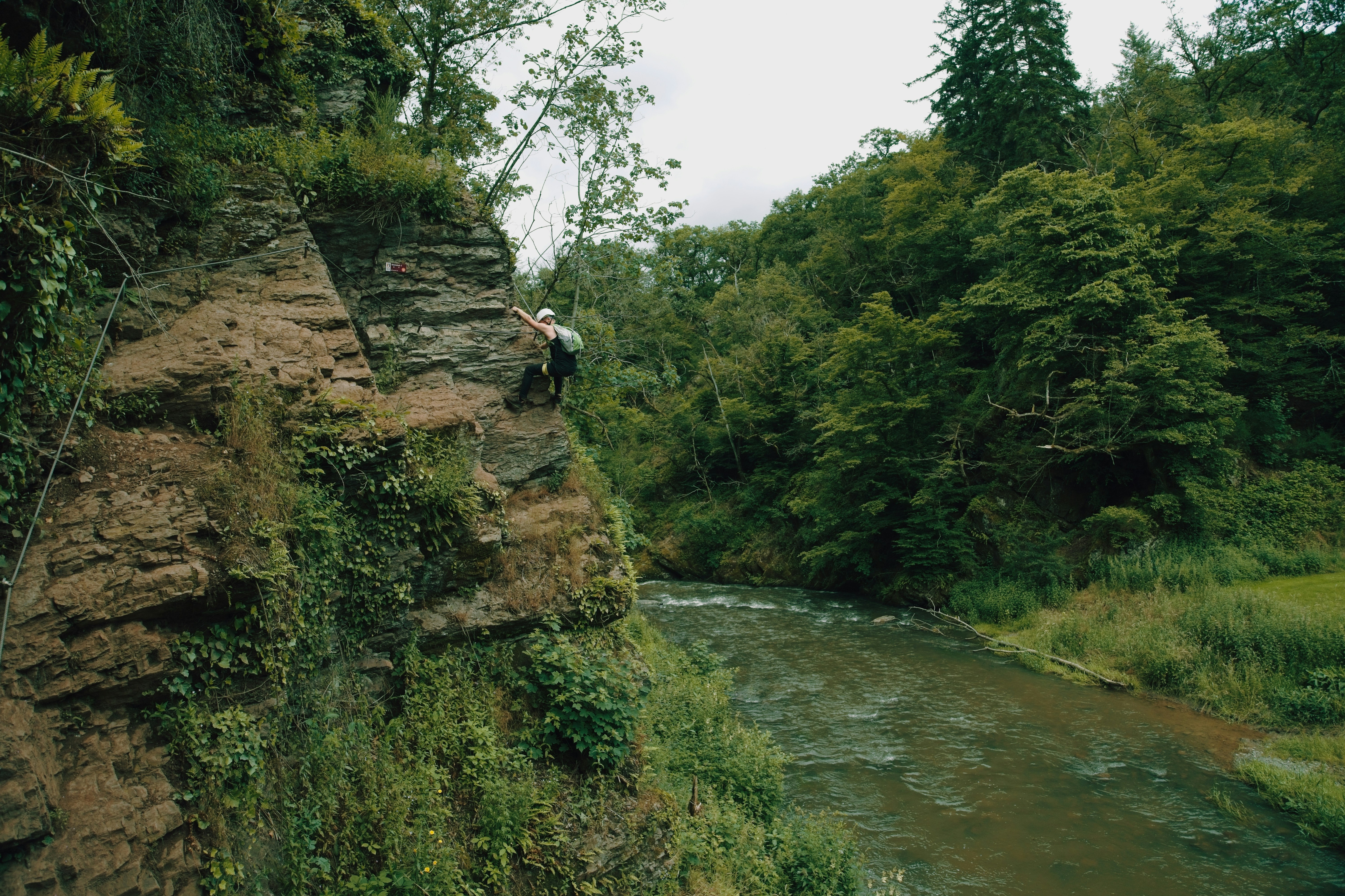 Climber Clings to a Moss-Covered Cliff Over a Rushing River Gorge