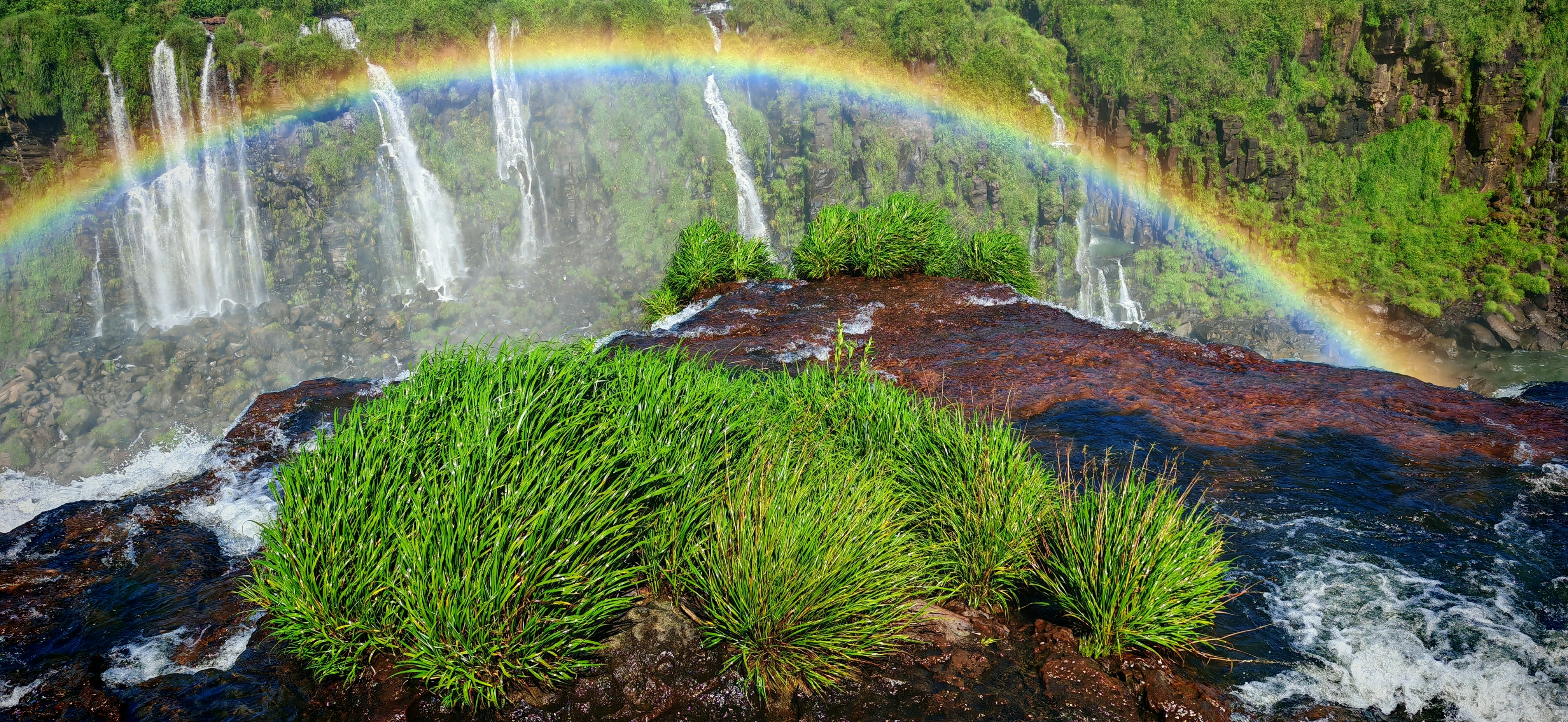 Rainbow over a lush green waterfall with rocky edges