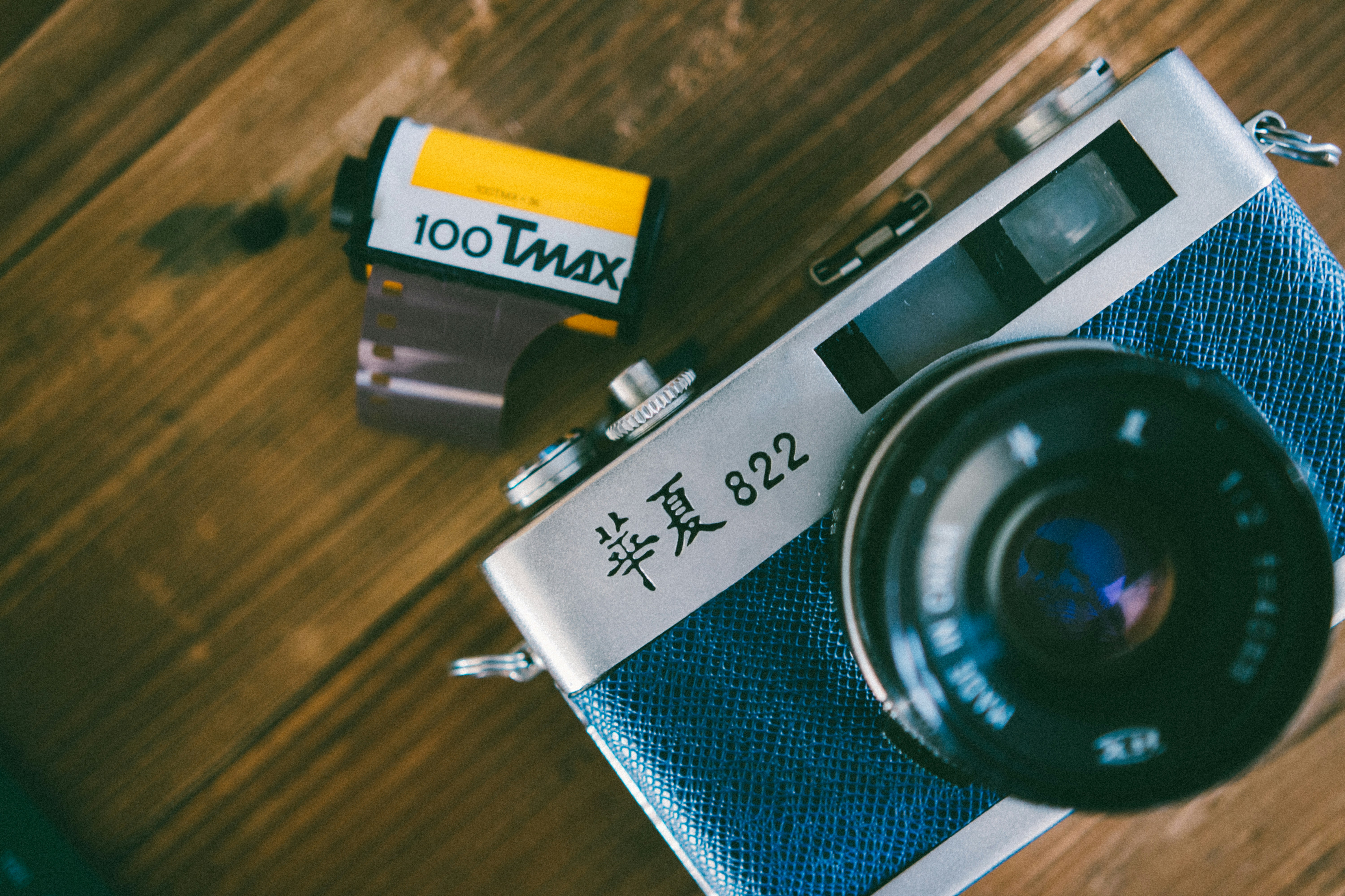 Blue Whisper: A Vintage SLR Resting by a 100 Tmax Film Can on Weathered Wood