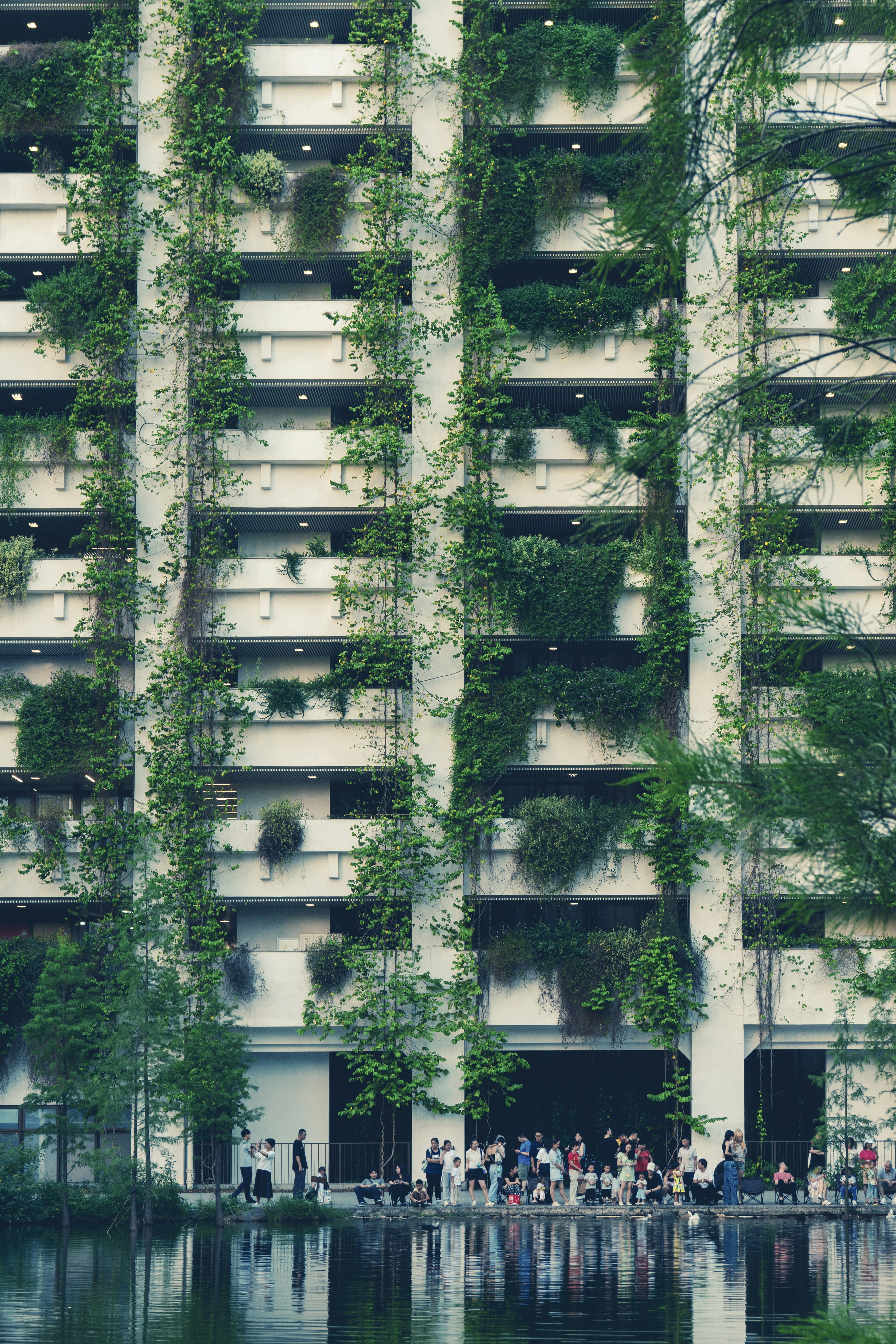 A building in a urban park with plants on its surface. Crowd gathers near it