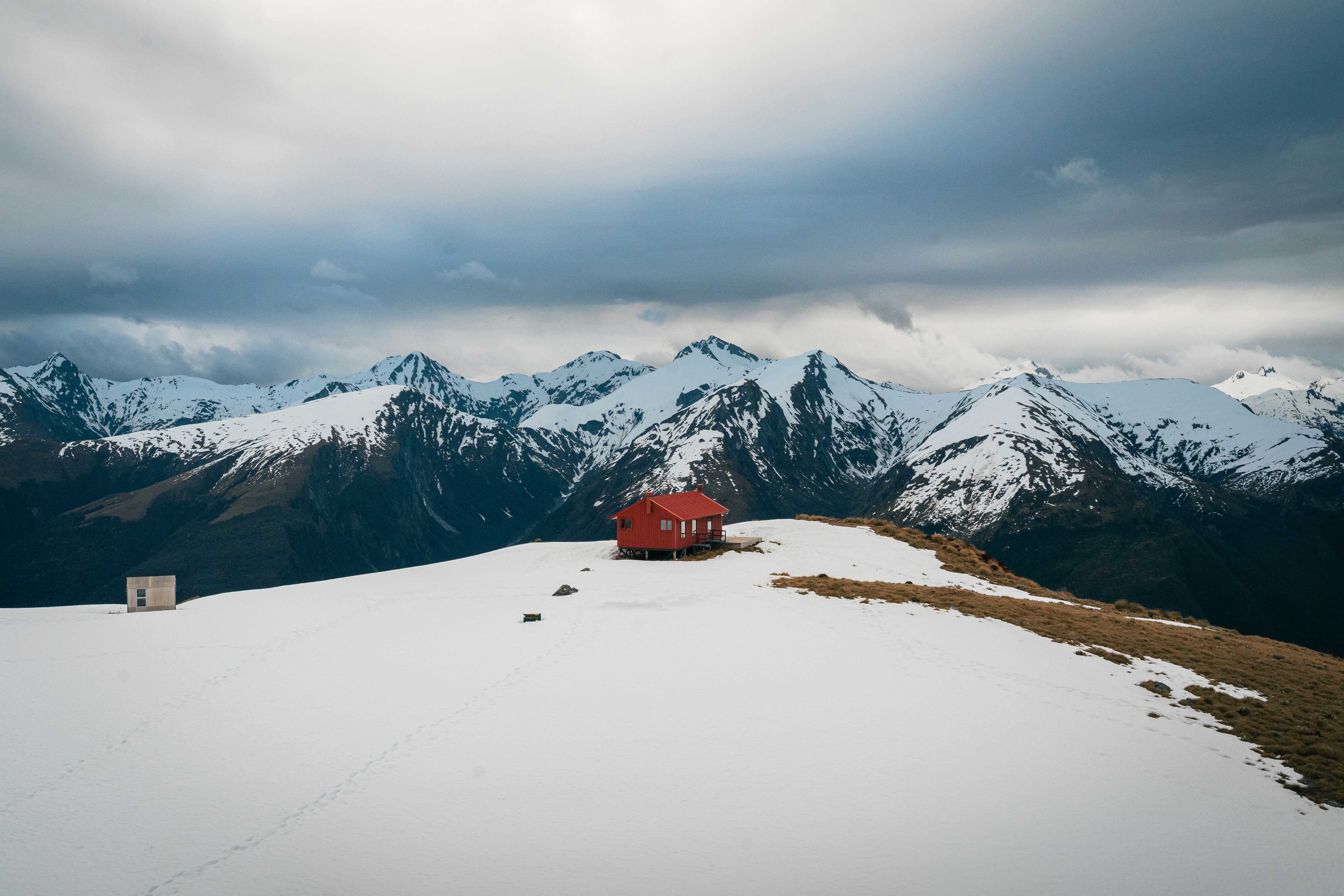 Red Cabin on a Snow-Covered Ridge Beneath Stormy Alpine Skies