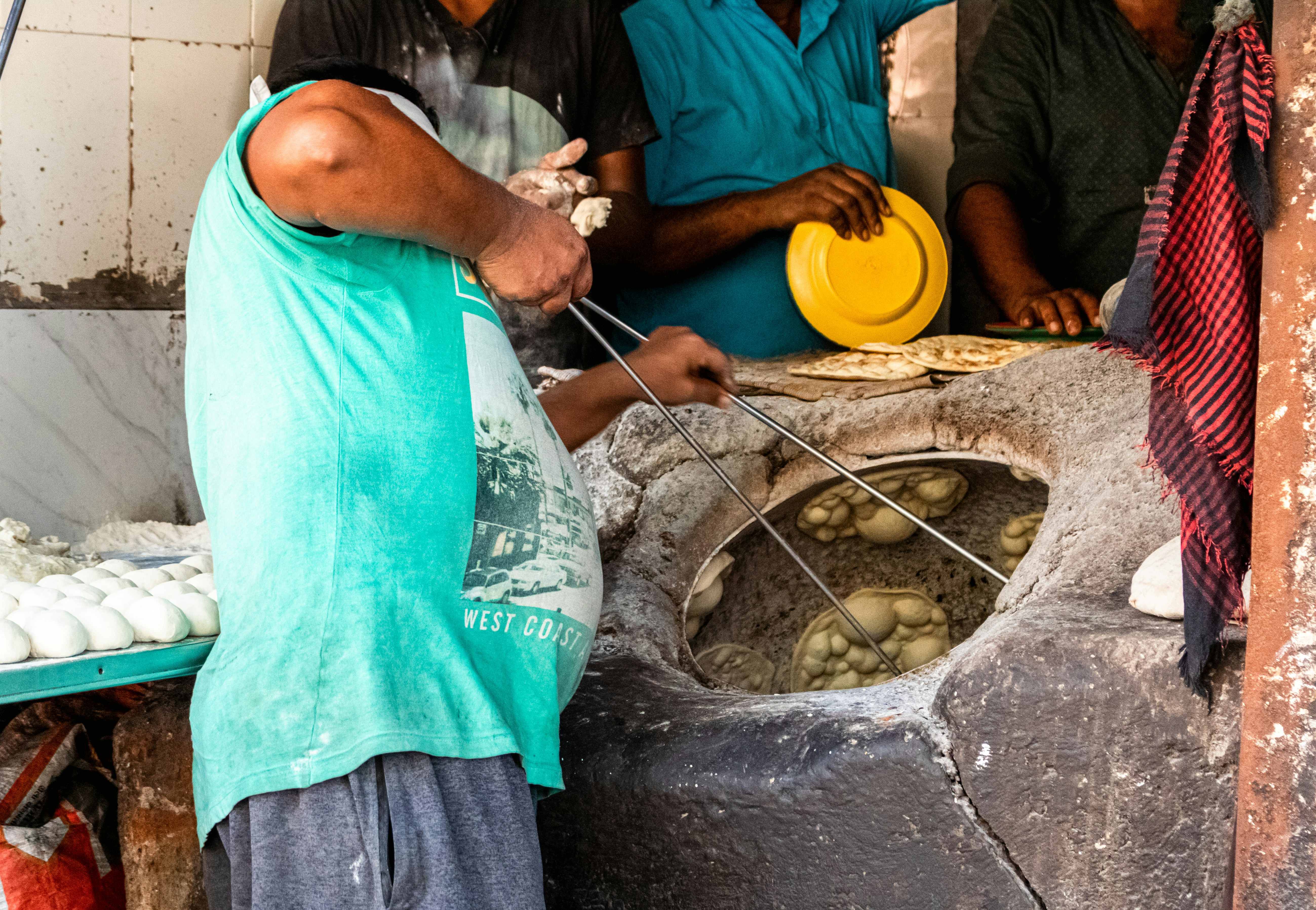 A mani is pulling out naan (flatbread) from the tandoor(a clay oven) with skewers.