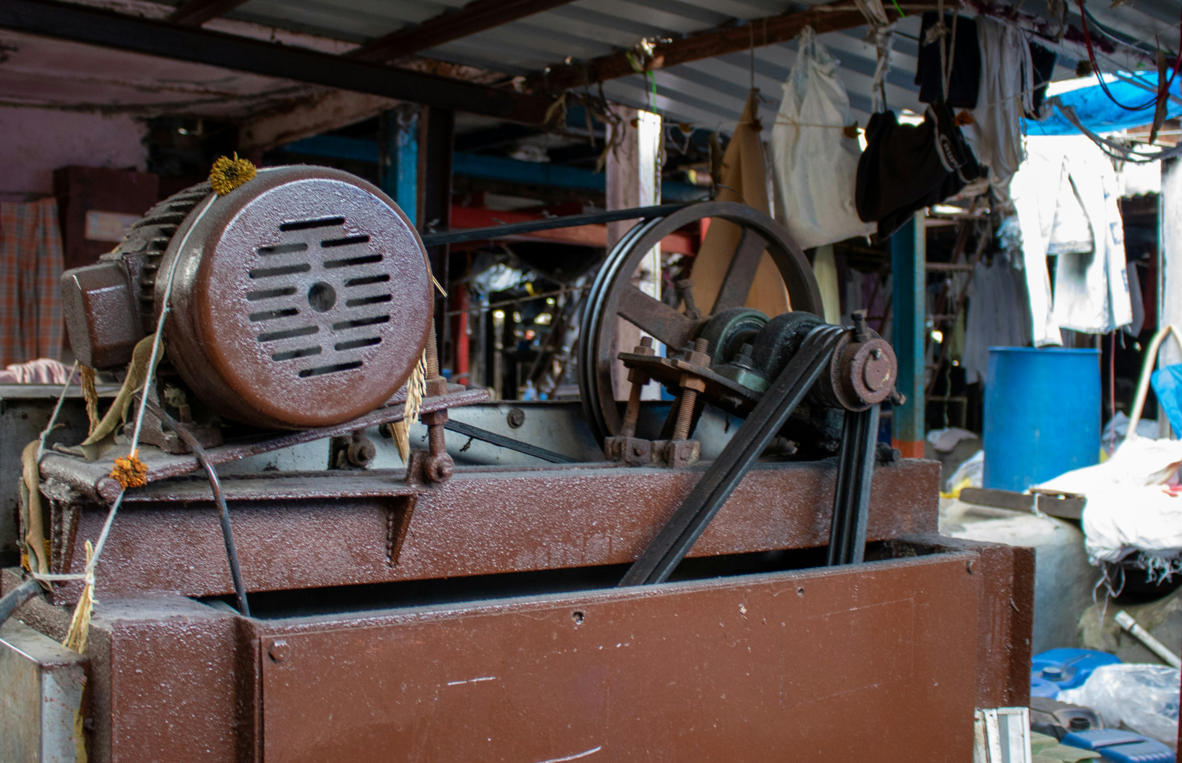 A close-up photograph captures an aged, heavy-duty industrial electric motor with a connected pulley and belt system, likely powering a piece of laundry machinery such as a washing machine or centrifuge.