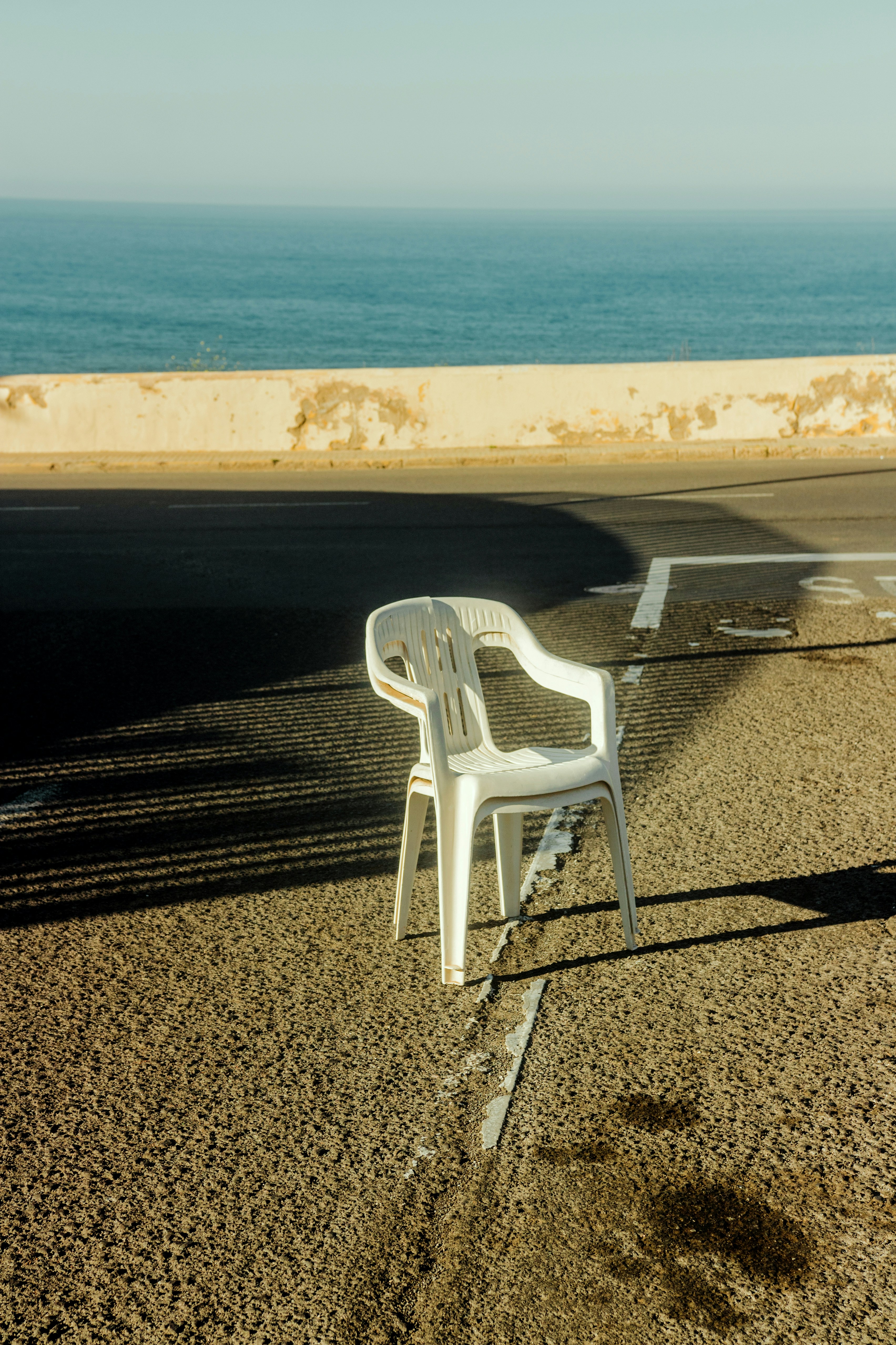 Solitary White Chair Along a Sea-Front Asphalt