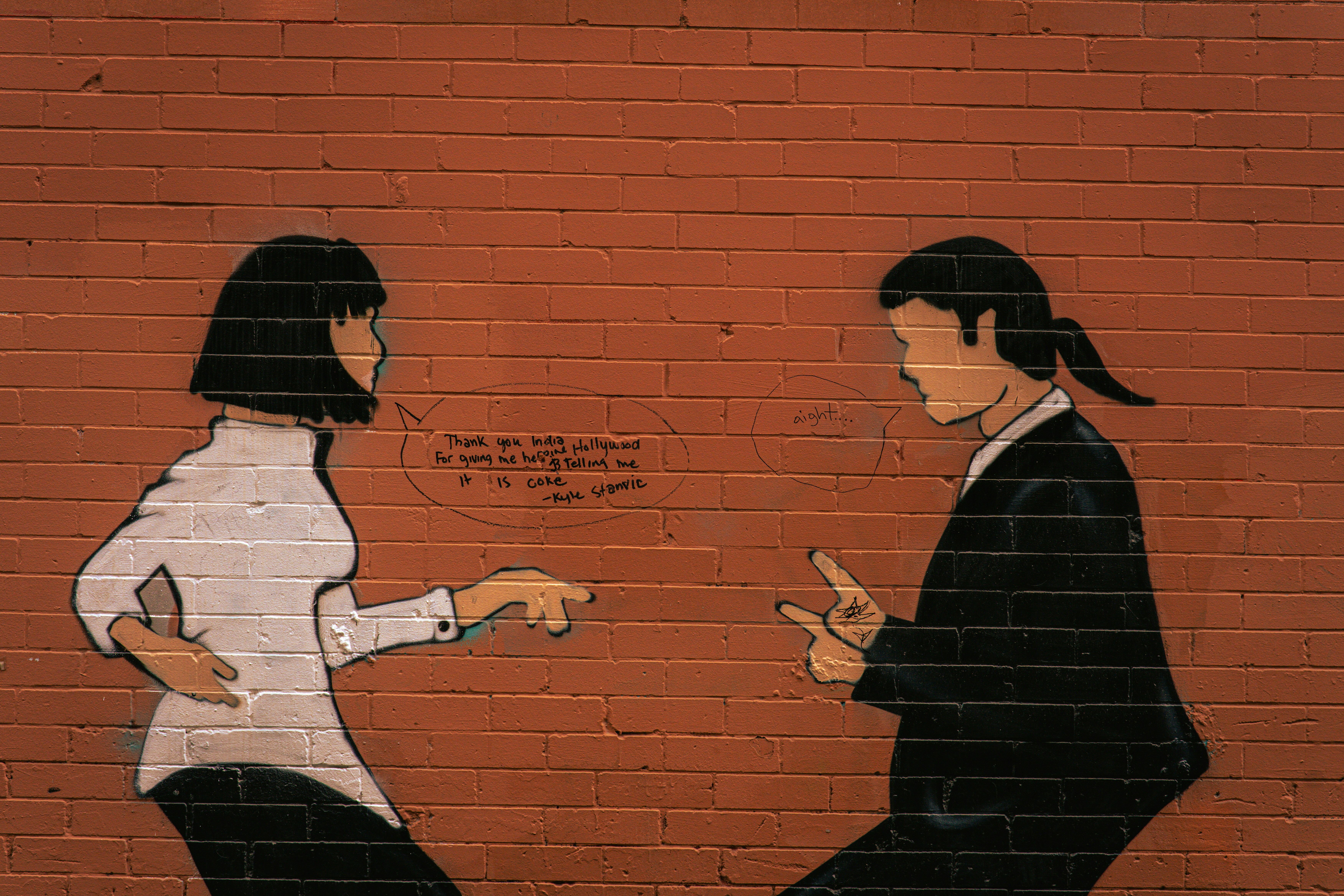 Two silhouettes on a brick wall share a quiet moment of mischief