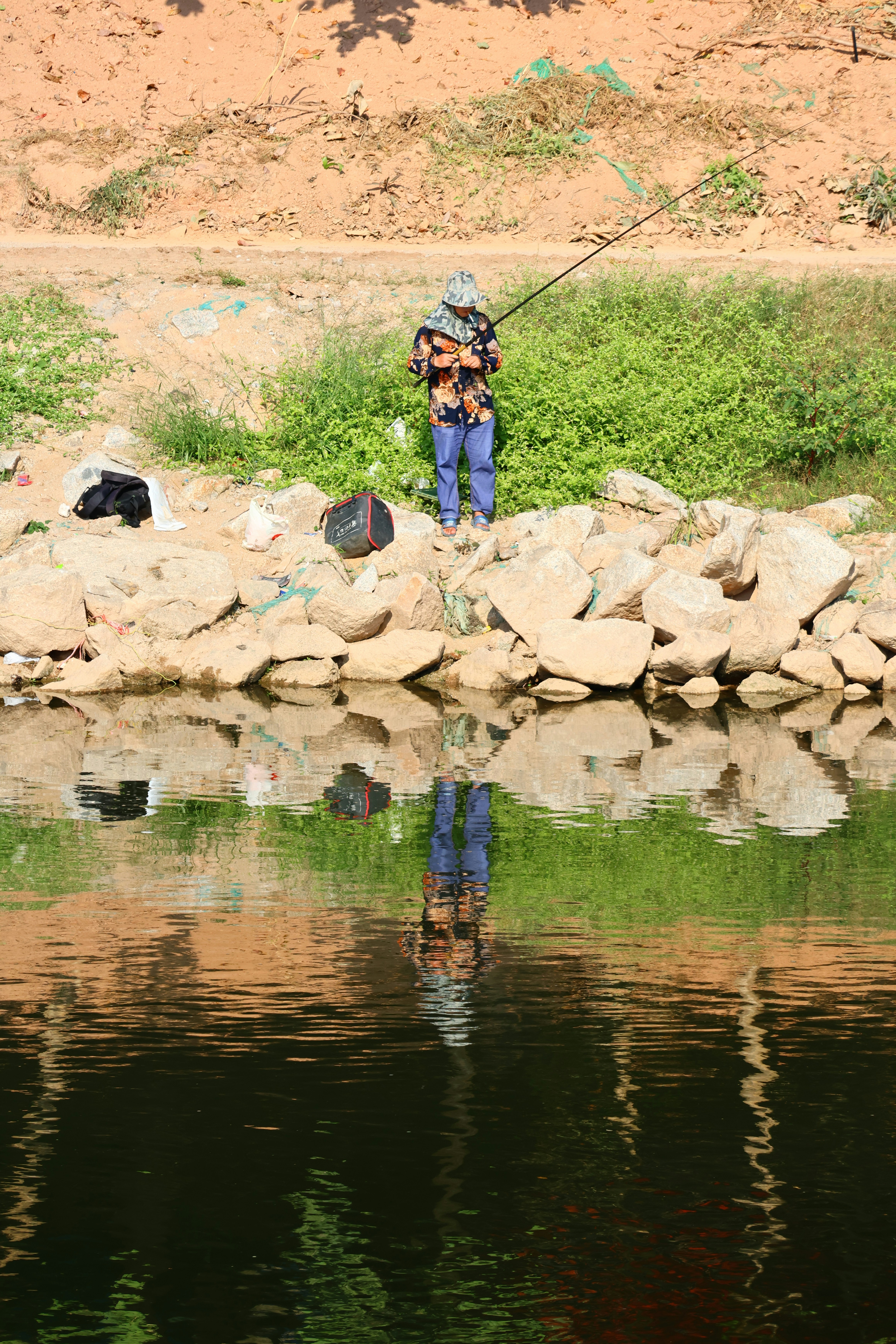 Echoes on the Riverbank: A Hat-Wearing Fisherman and His Reflection