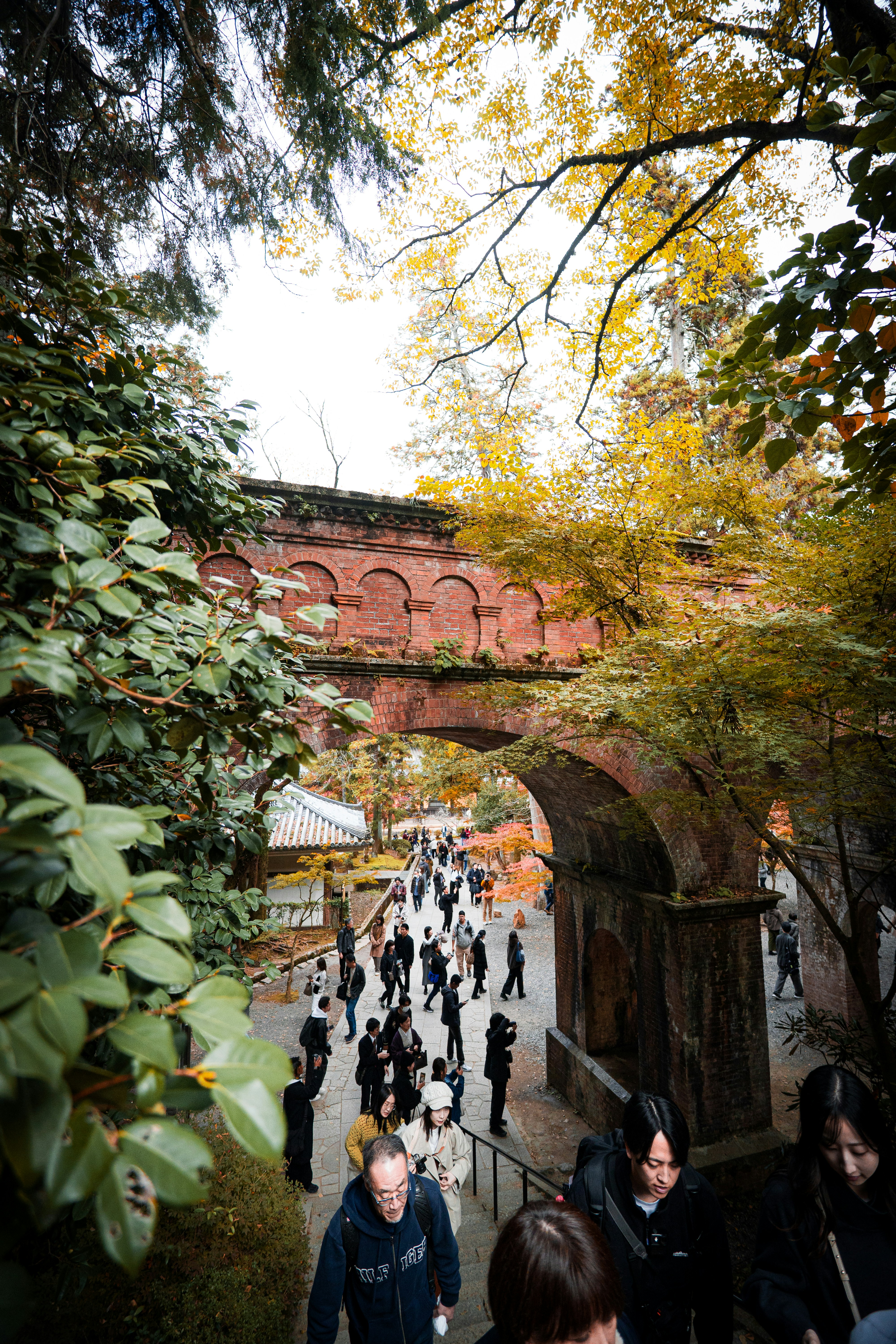 Archway Rendezvous: People Thread Through Autumn Under a Red Brick Bridge