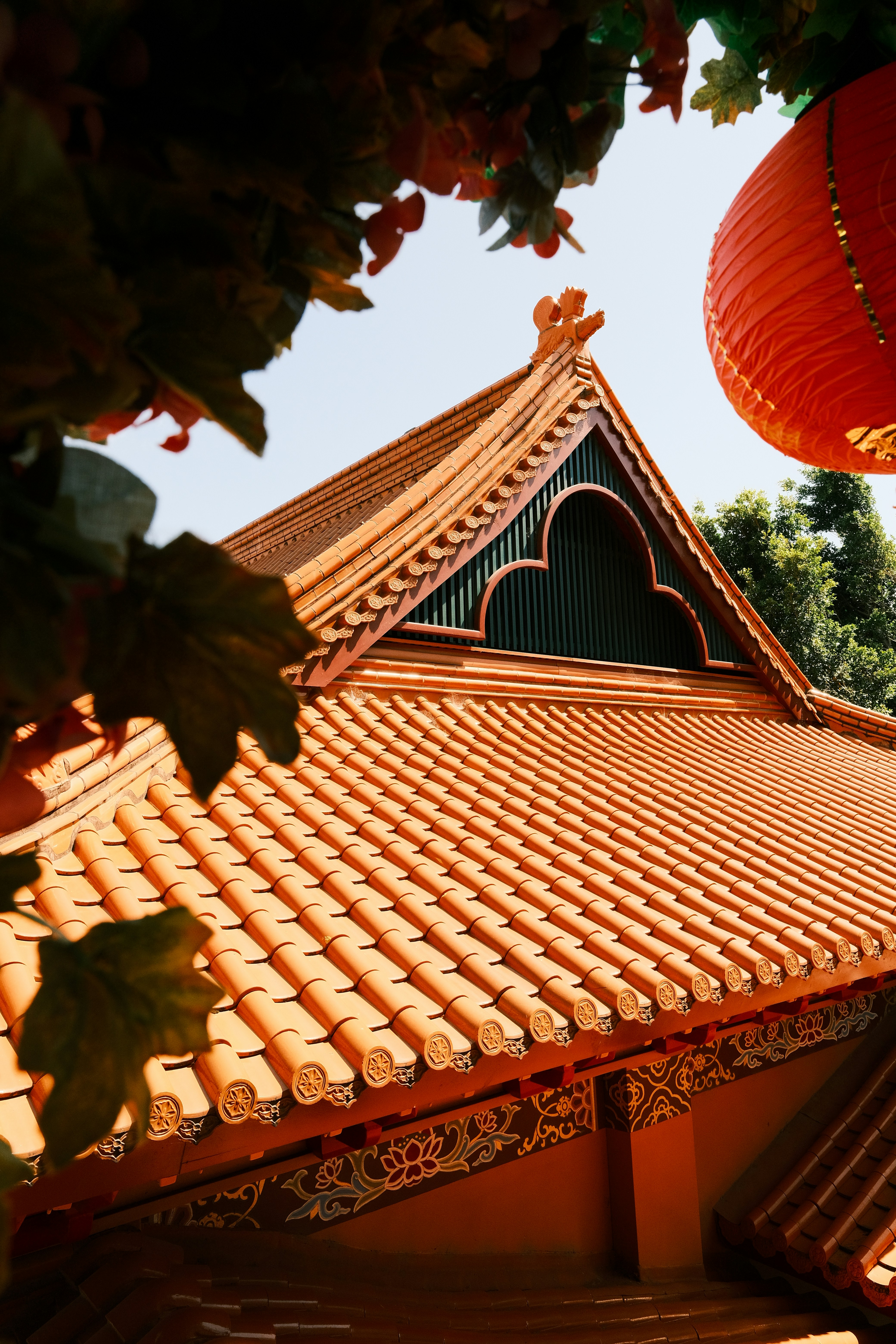 Autumn Framing: A Red Lantern Adorns a Sunlit Orange-Tiled Temple Roof