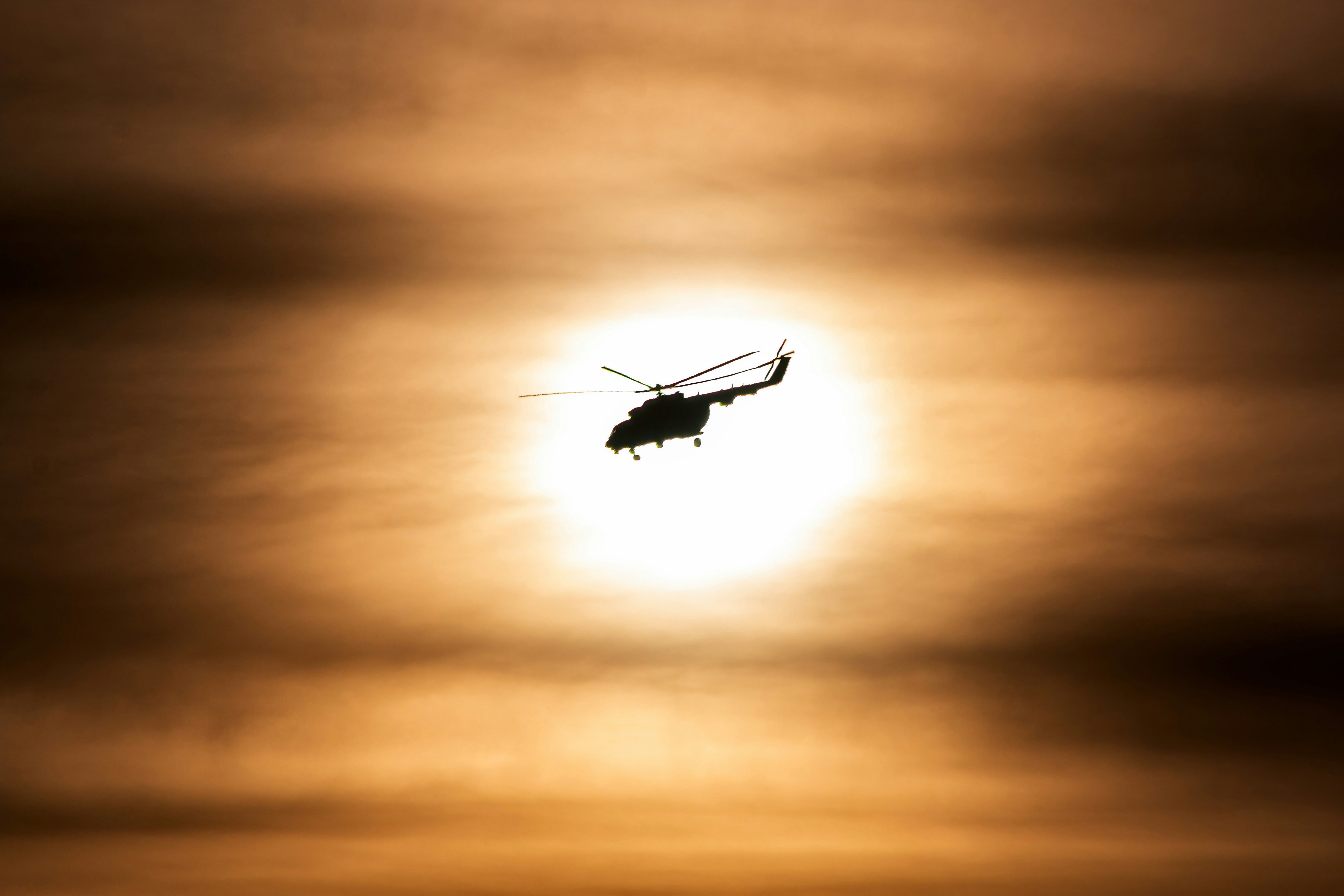 Silhouette under an amber sun: a helicopter crossing a fiery horizon.