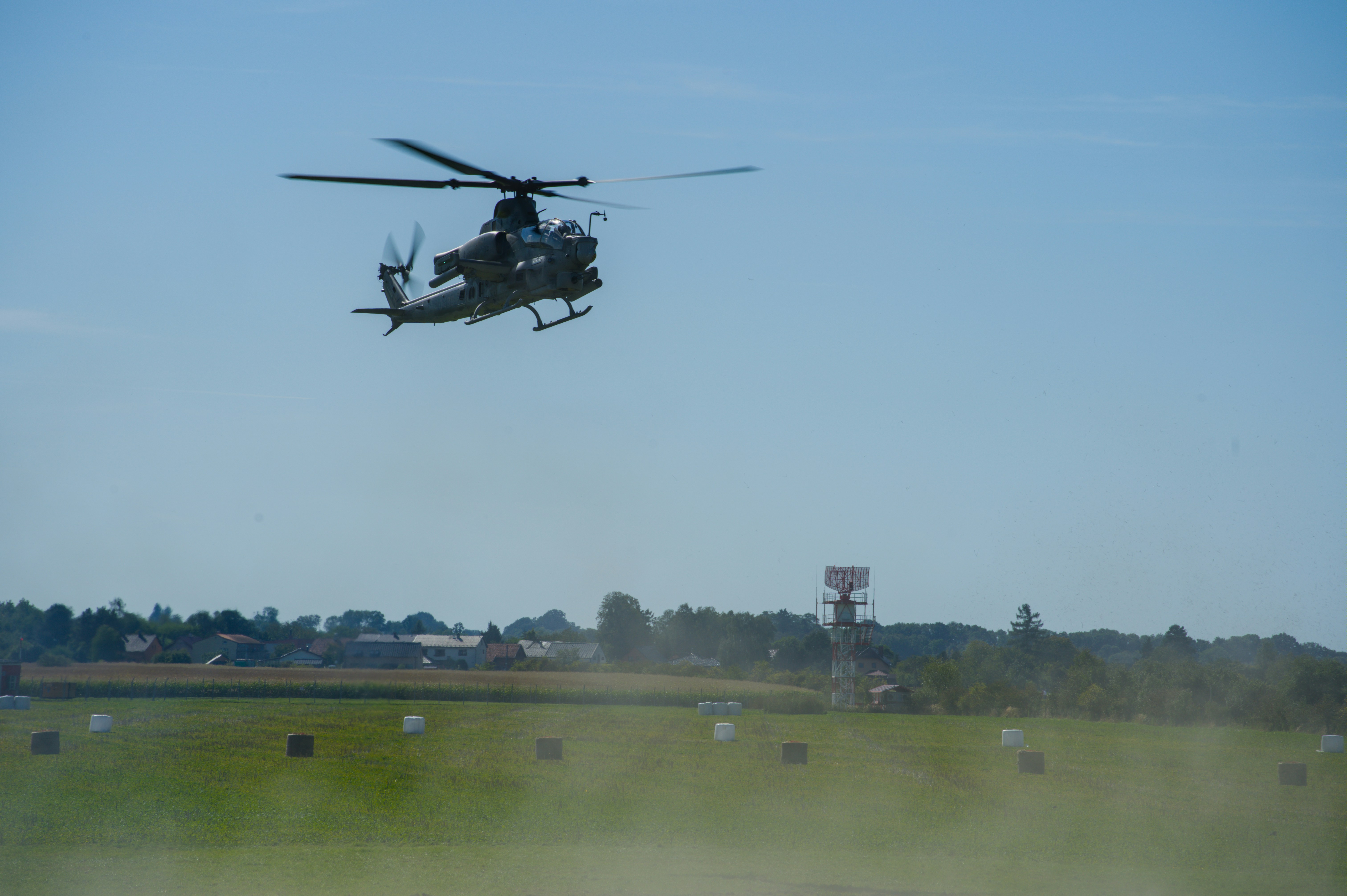Hovering rotorcraft over a dusty airfield under a clear blue sky.