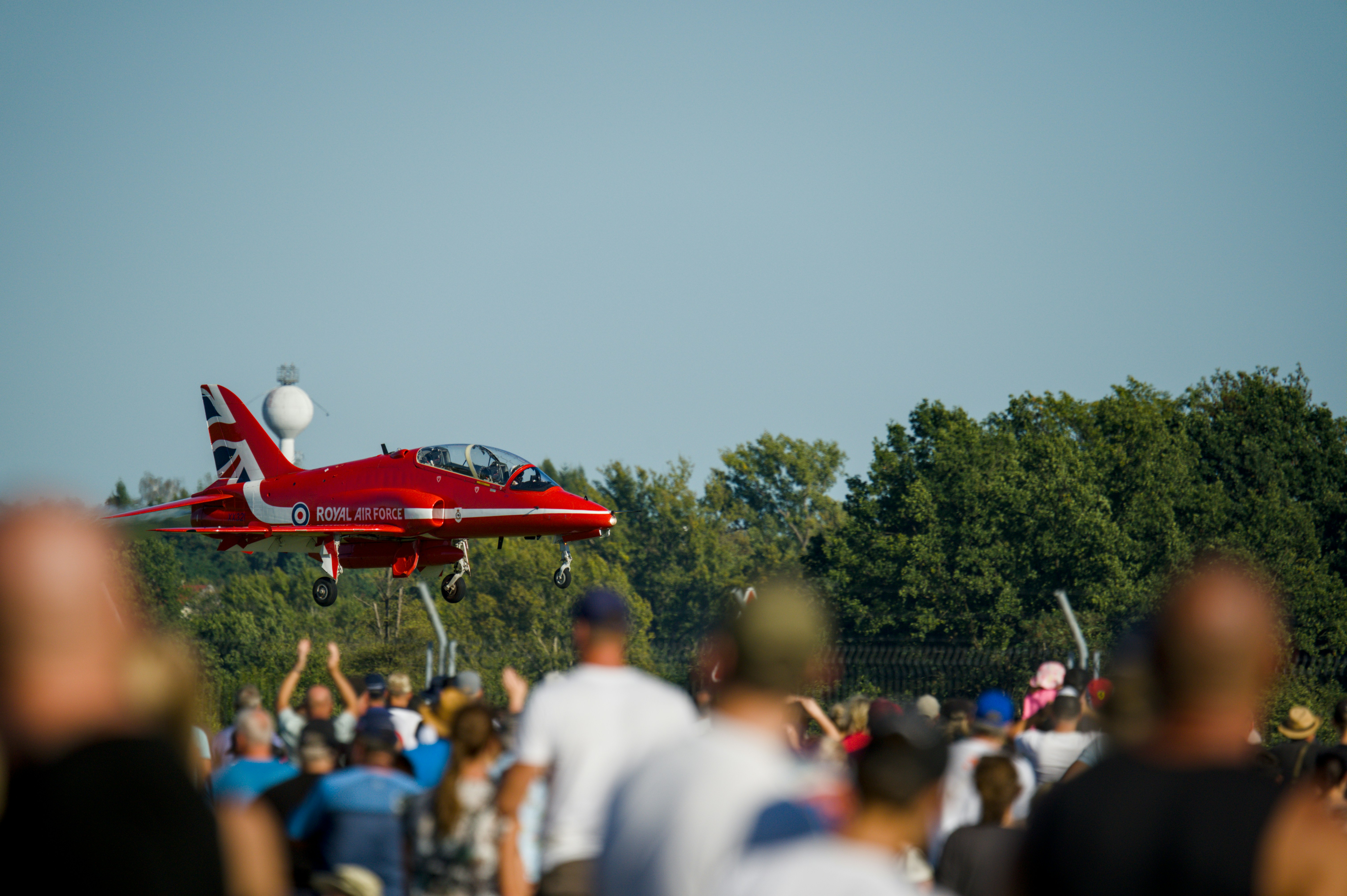 Crimson Jet Rises Over a Sea of Hands at a Sunlit Airshow