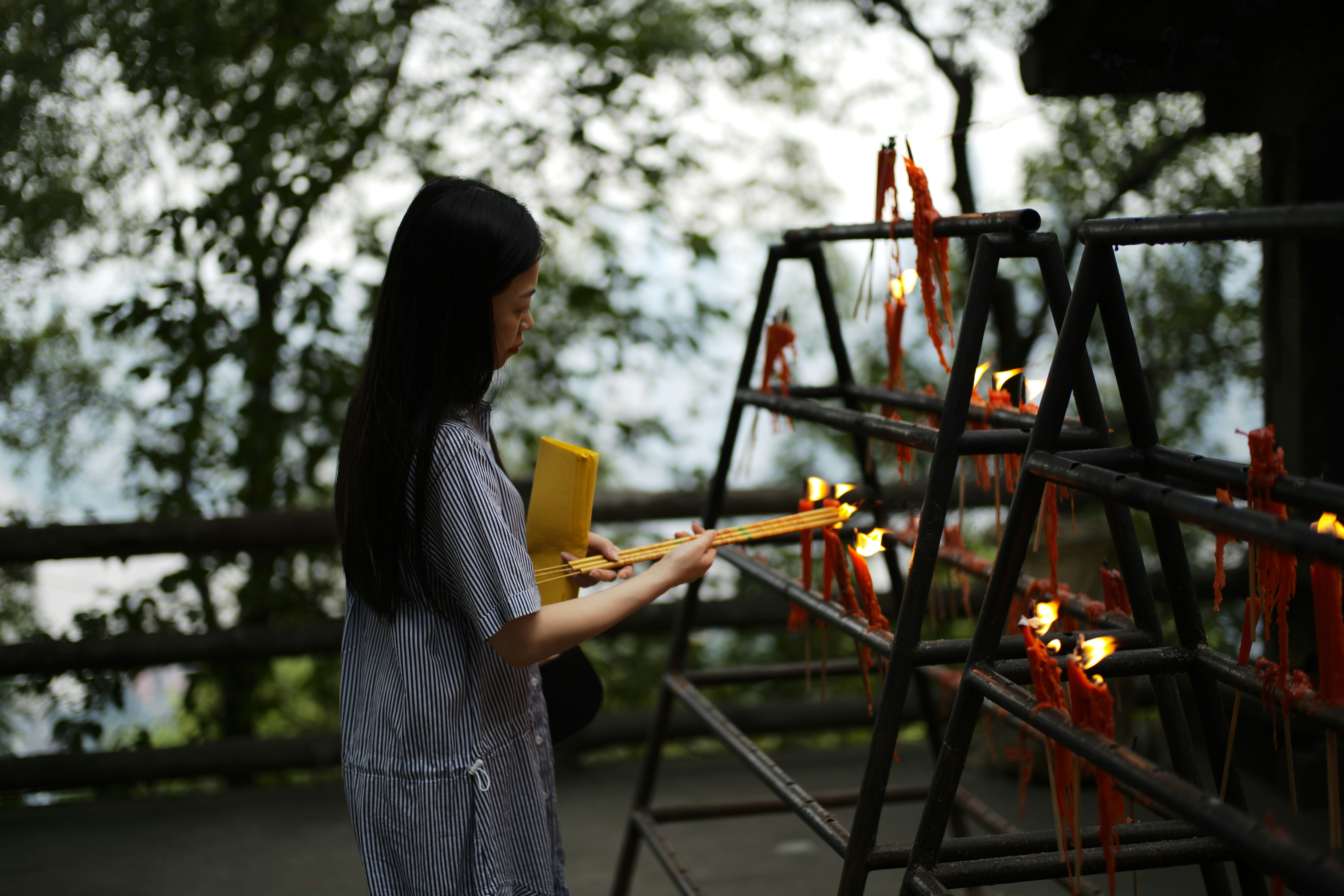 Woman lighting candles at an outdoor shrine.