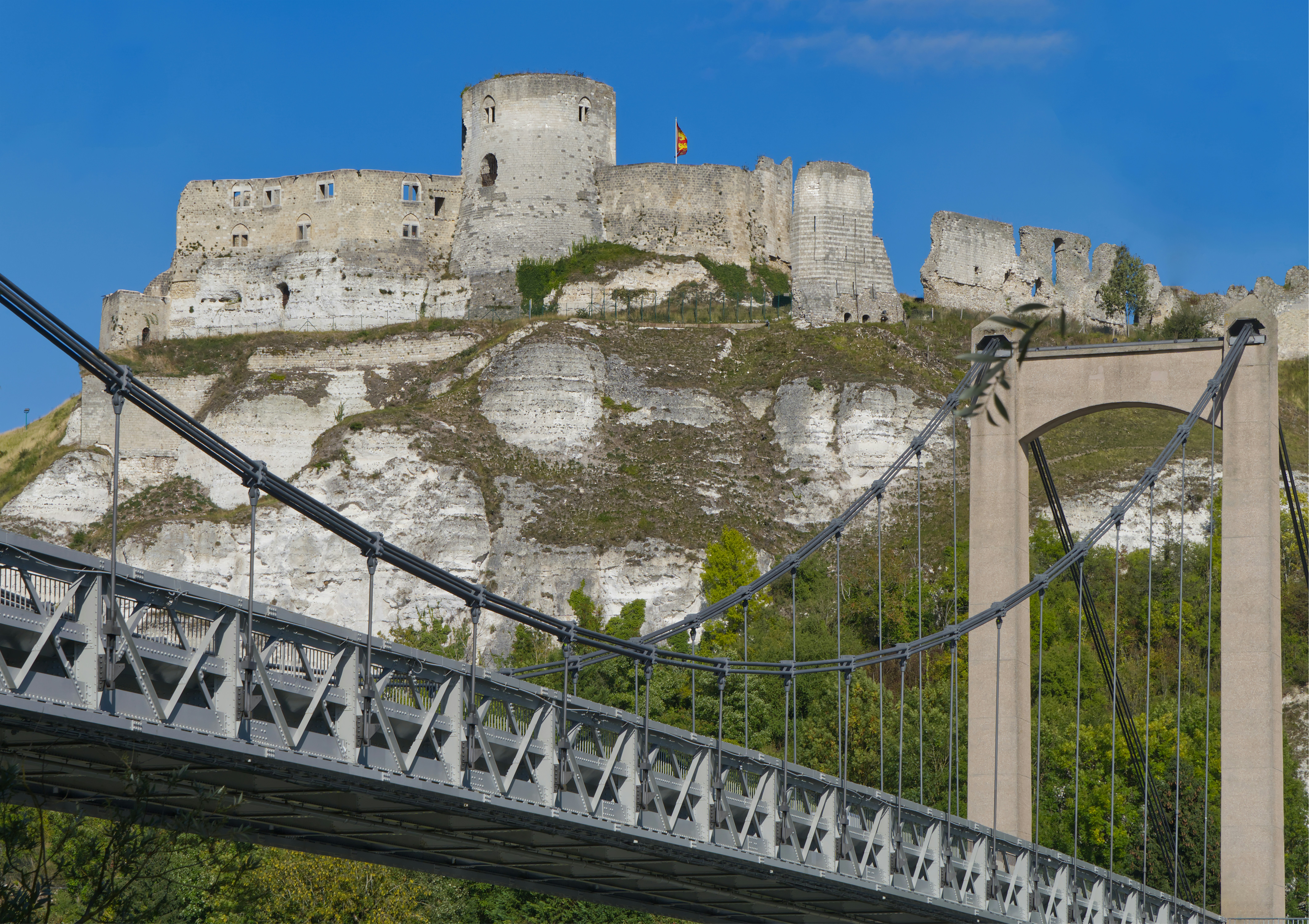 Contre-plongée sur Château-Gaillard. Construit entre 1196 et 1198 par Richard Cœur de Lion, roi d’Angleterre et duc de Normandie, le château avait pour but de protéger la Seine et la ville de Rouen des prétentions du roi de France, Philippe Auguste. Le château surplombe un méandre de la Seine, offrant une position stratégique exceptionnelle. Cet édifice s’inscrit dans la rivalité entre les rois de France et les rois d’Angleterre, ducs de Normandie, qui se disputent le contrôle de la région depuis les années 1060. Après la mort de Richard Cœur de Lion en 1199, son frère Jean sans Terre lui succède. Philippe Auguste en profite pour relancer la conquête de la Normandie, et assiège Château Gaillard en 1203. Après un long siège, la forteresse tombe en 1204, marquant la fin de la domination anglaise sur la Normandie.