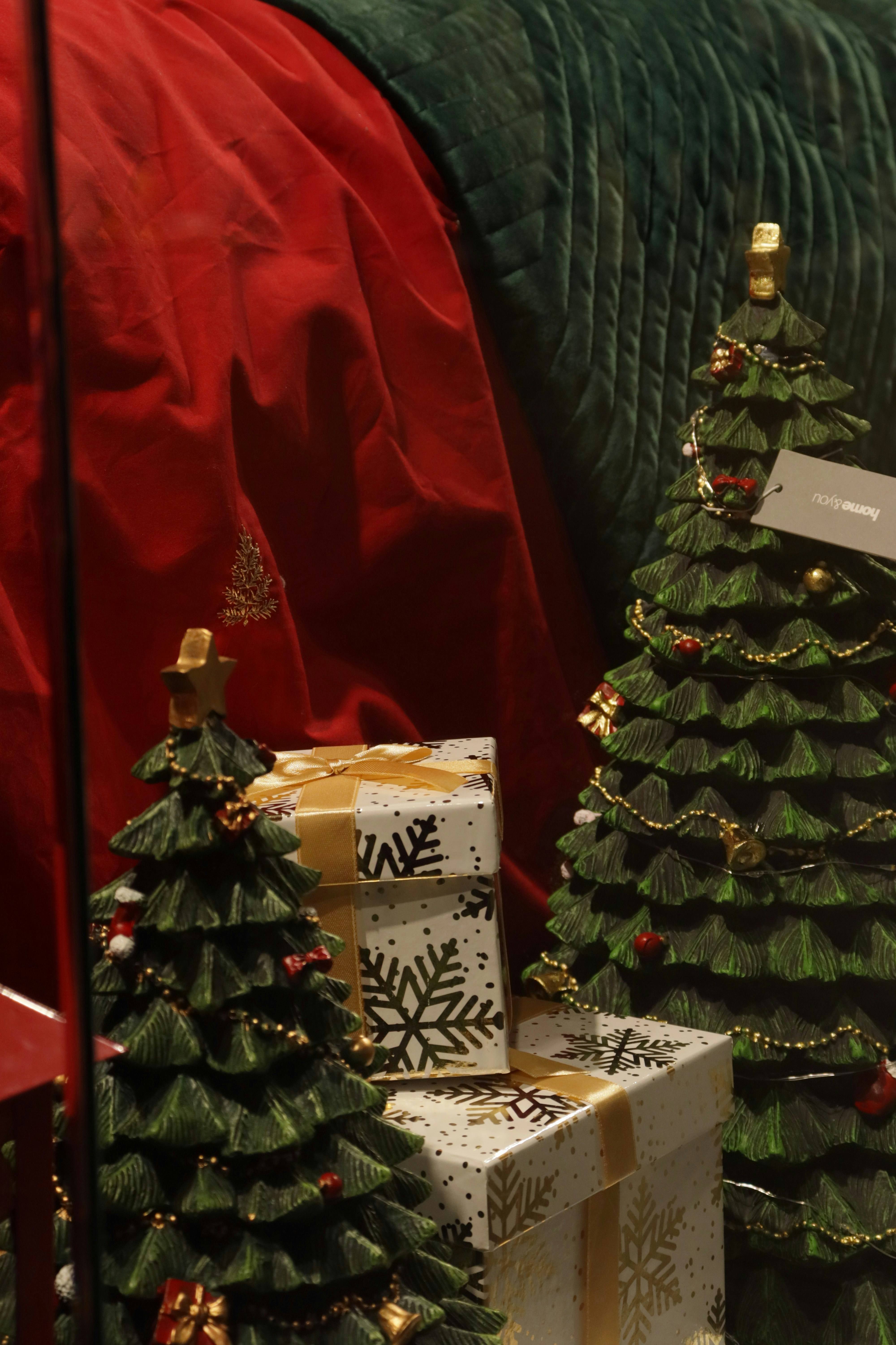 Miniature Christmas trees stand beside gift-wrapped boxes with snowflake patterns against a red velvet backdrop.