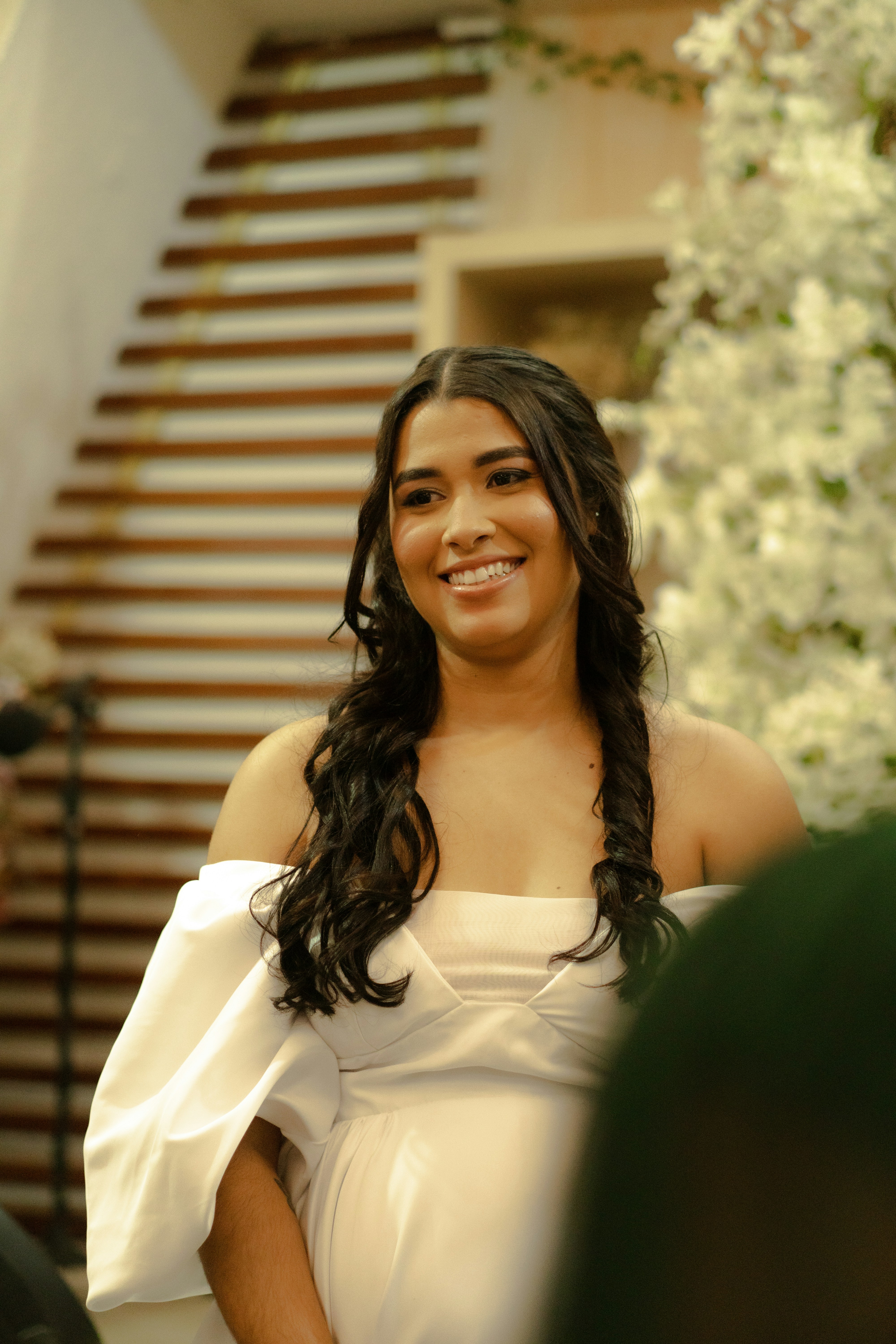 Bride in Off-Shoulder White Gown Smiles Amid Floral Backdrop