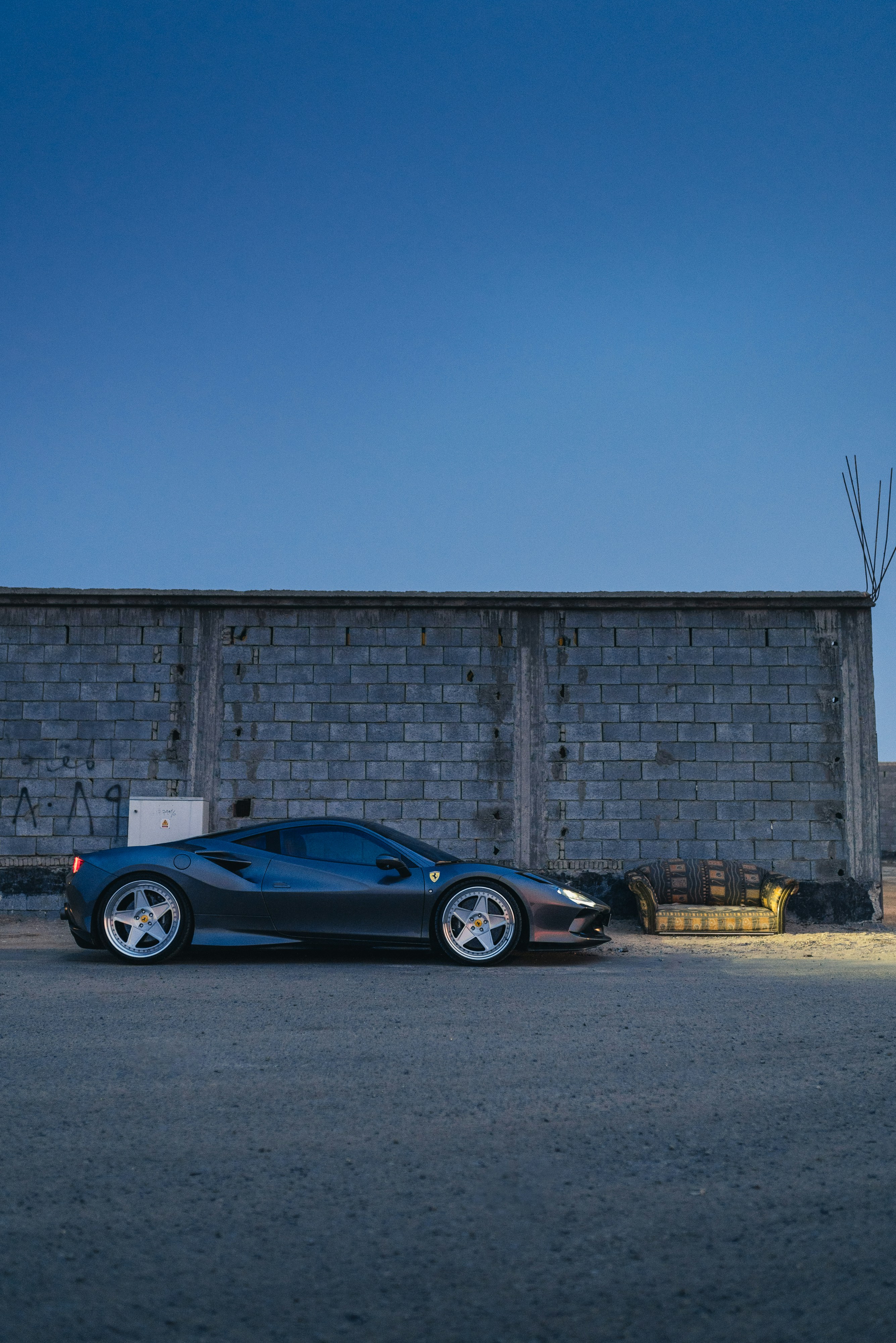 Low-slung blue supercar rests along a weathered industrial wall