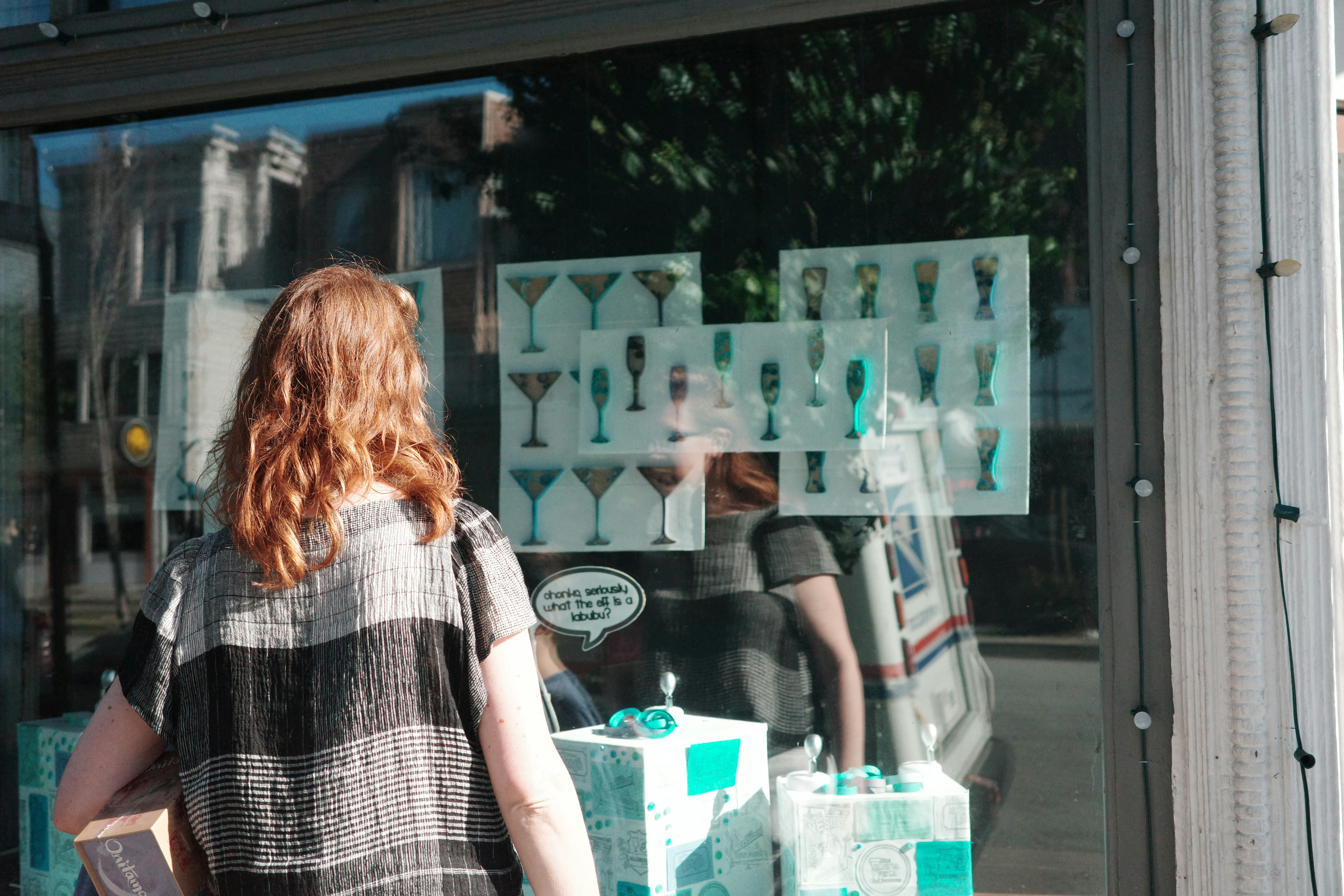 Street-level Window Watch: A Woman with Striped Shirt Faces a Display of Turquoise Glassware