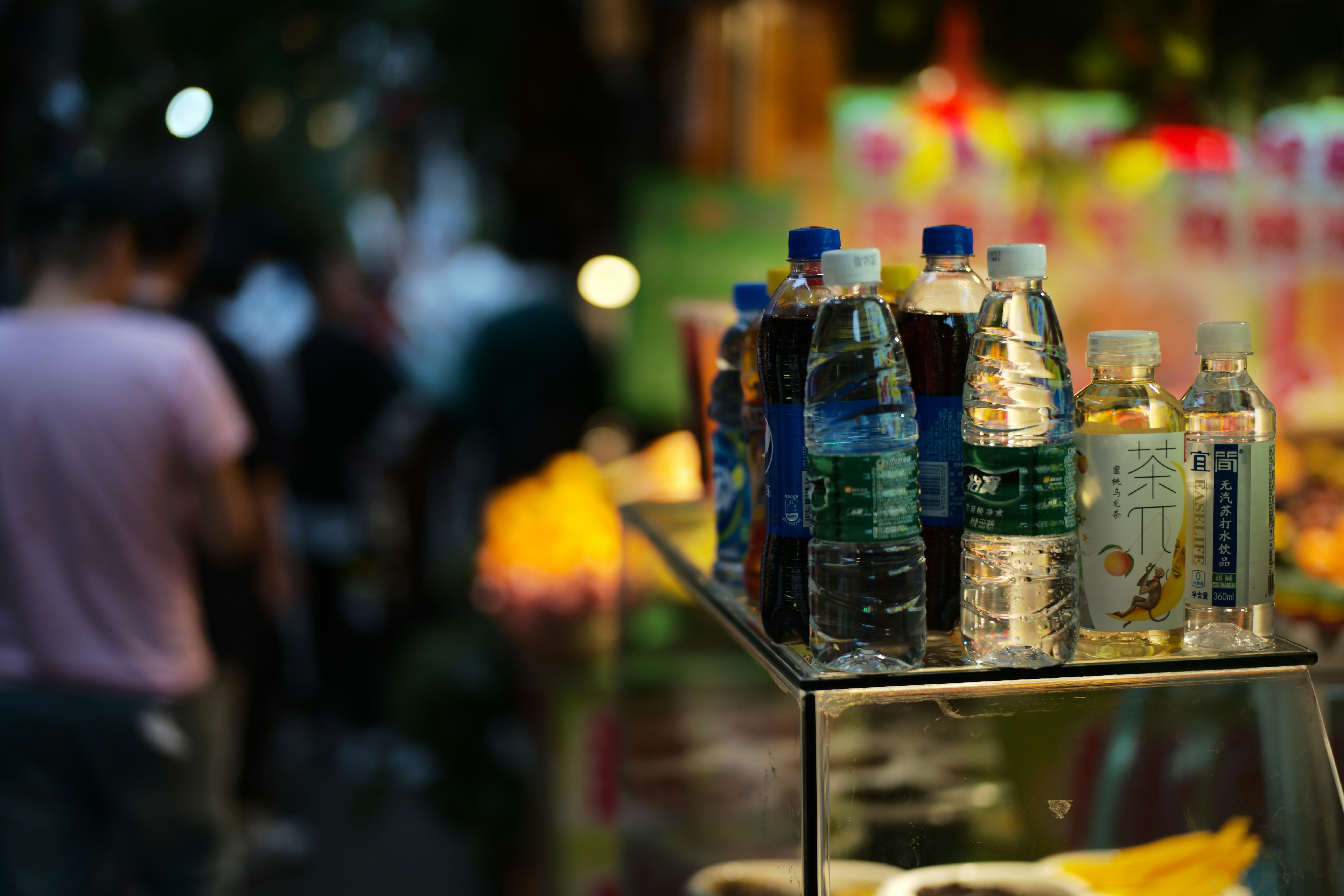 Bottled beverages line a chrome cart at a bustling street market