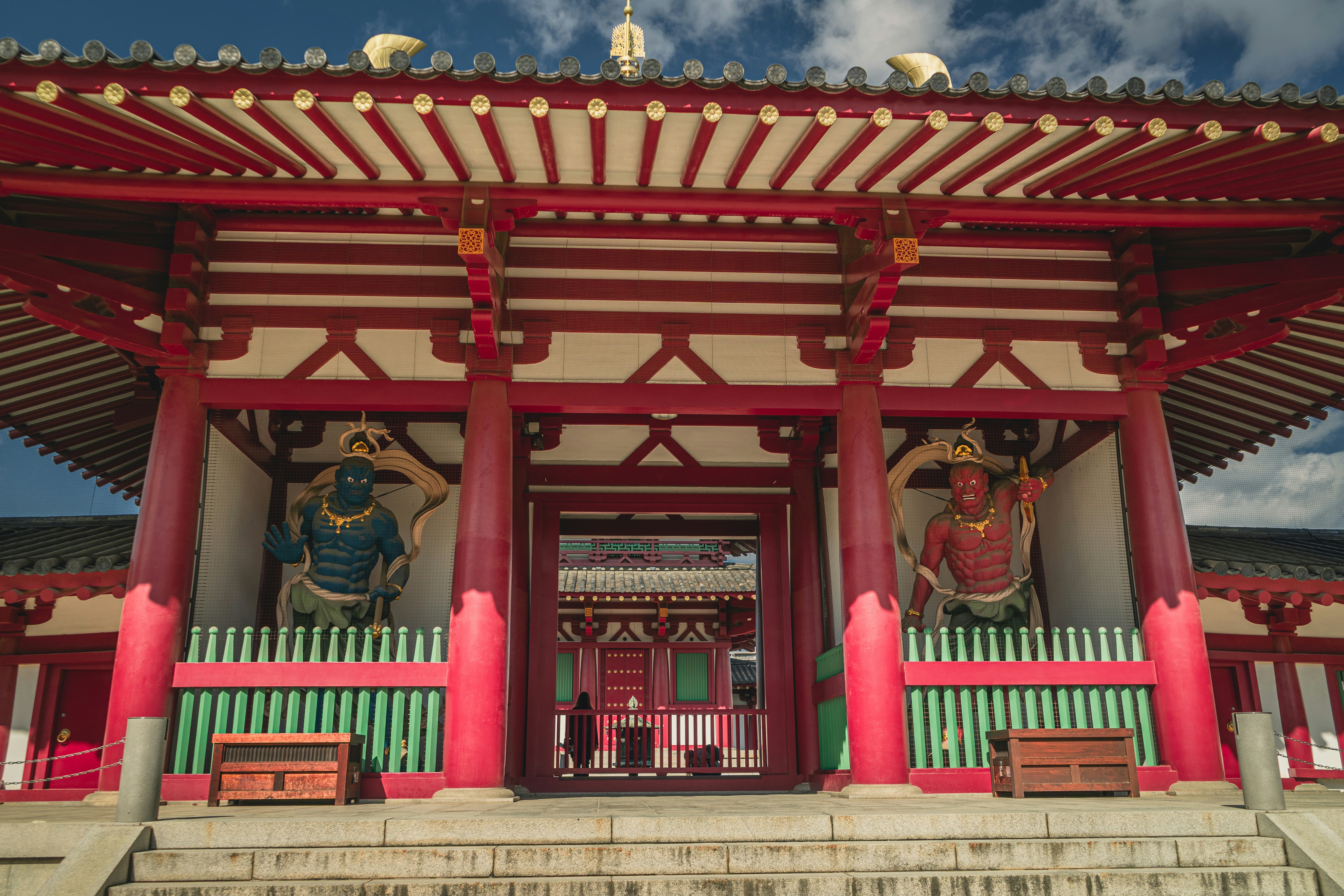 Two Nio guardian statues - Agyo (red, with open mouth) and Ungyo (blue, with closed mouth) - stand watch at the entrance of Shitennoji Temple in Osaka. These fierce protector deities represent traditional Buddhist symbolism and Japanese temple art.