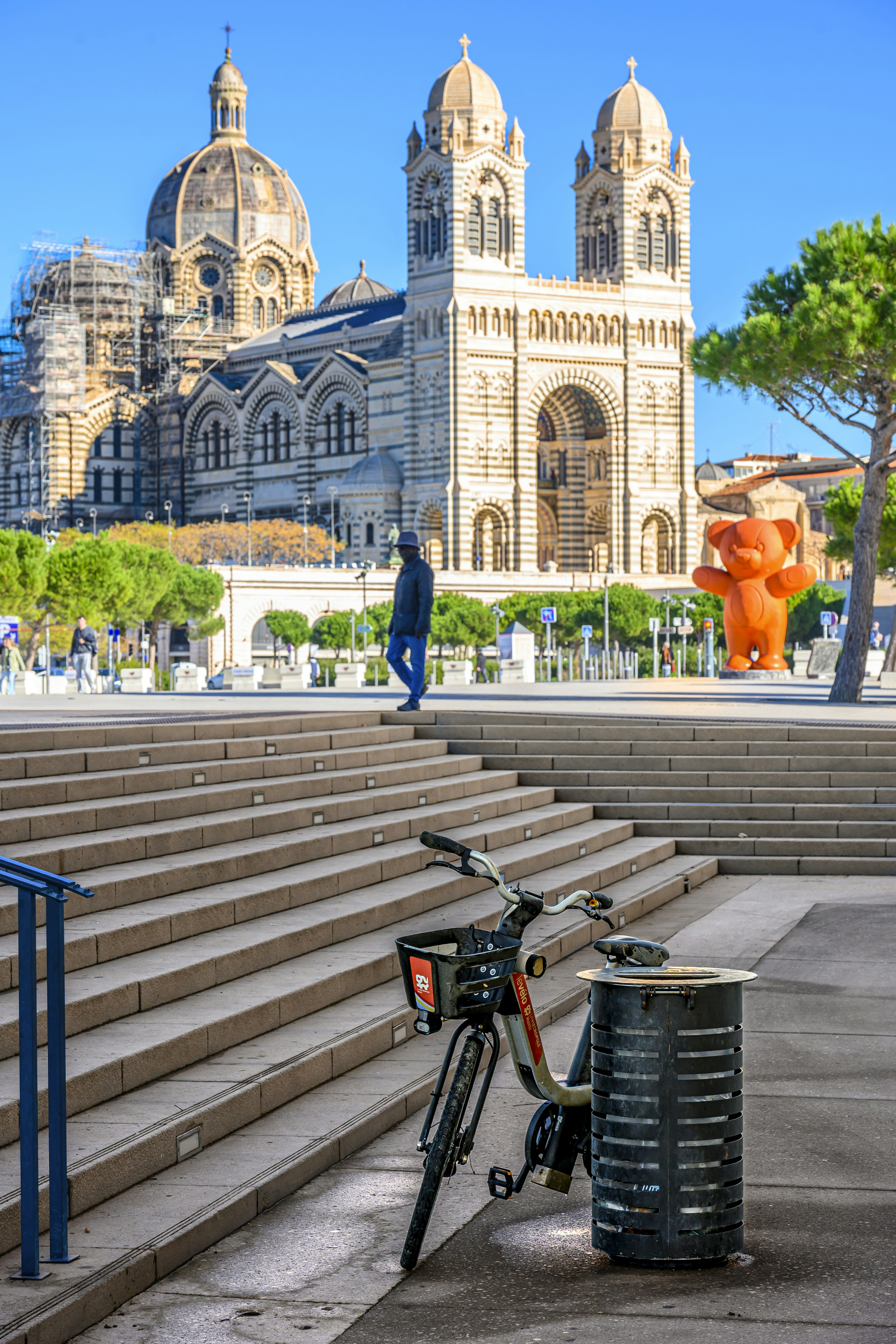 Blue Skies Over a Striped Cathedral: Steps, a Bicycle, and an Orange Sentinel