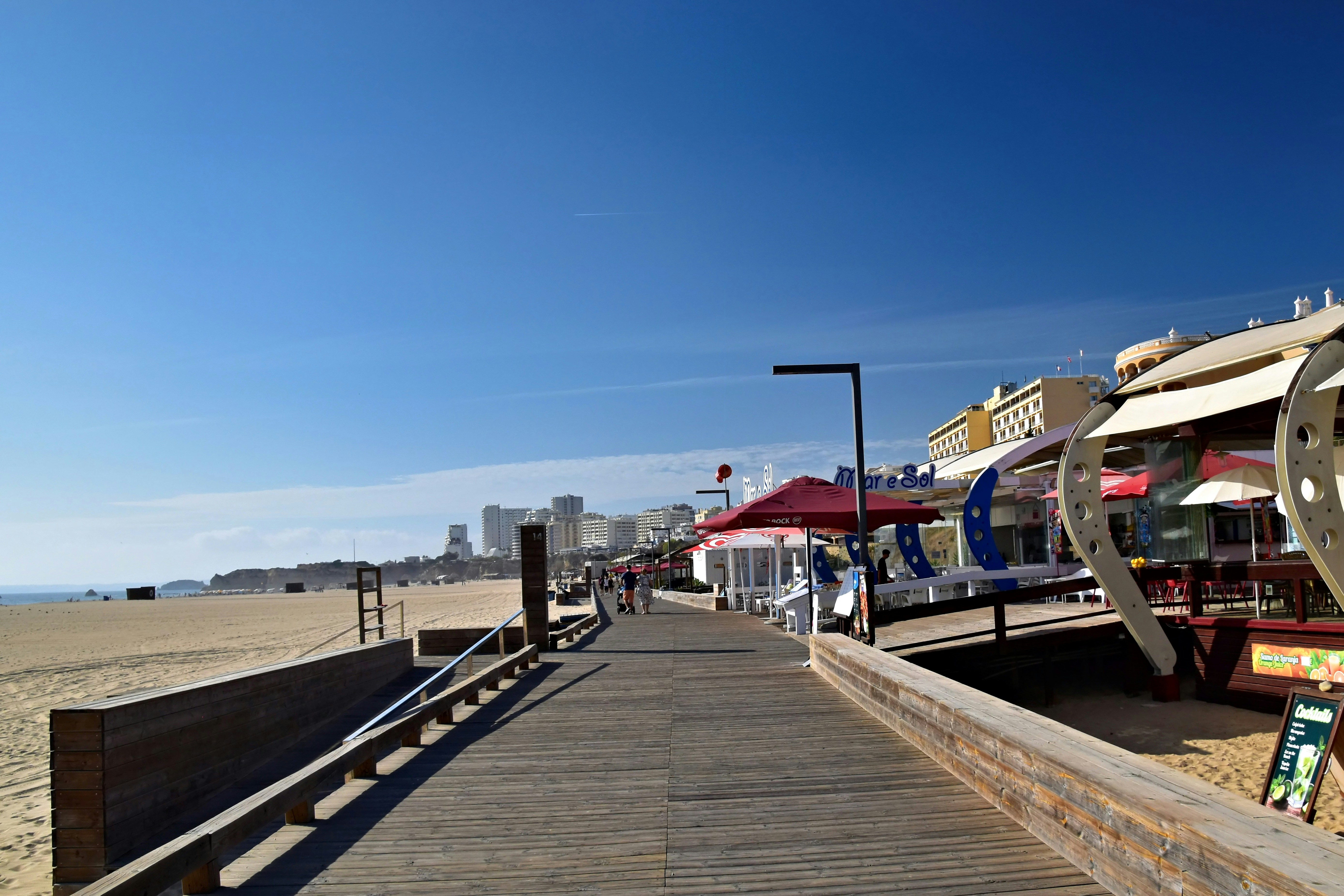 Sunlit Pierfront Parade: A Coastal Boardwalk Under a Clear Blue Sky