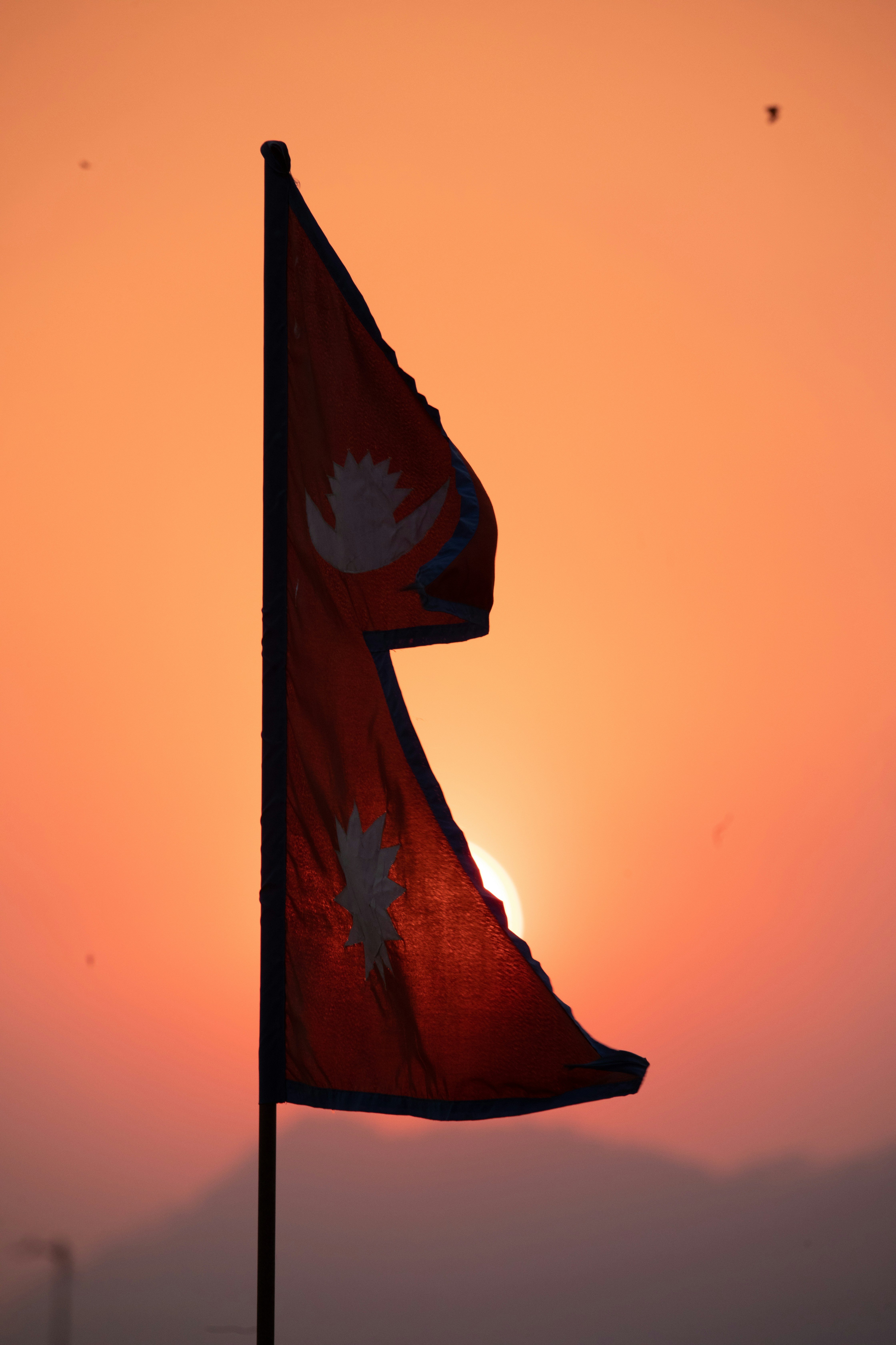 Flag in silhouette at sunset: a quiet Nepal flag against a glowing horizon