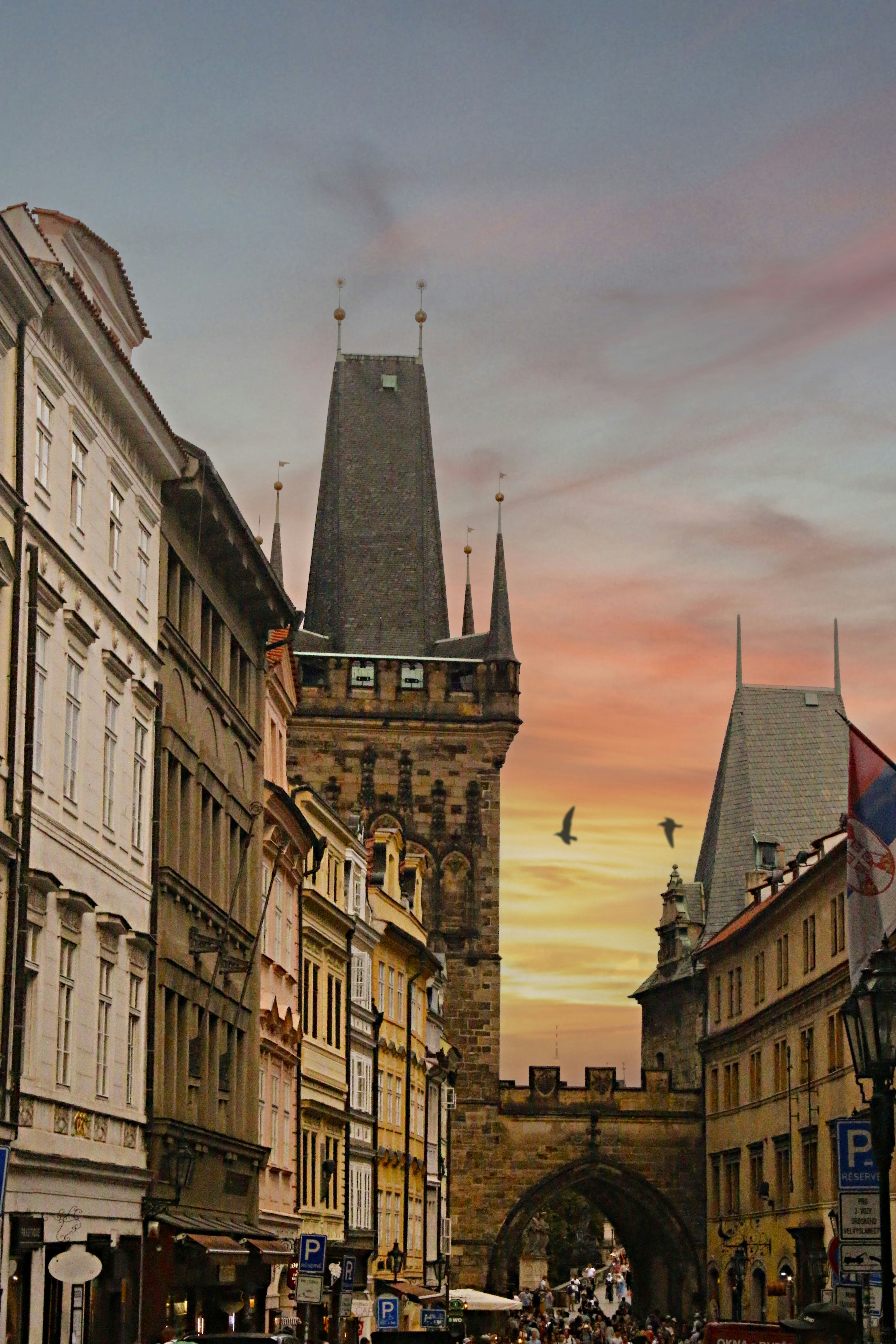 The Old Town Bridge Tower, one of the historic gateways to Charles Bridge, rises imposingly as the sky turns warm shades at sunset. The medieval and baroque facades frame the path, creating a magical atmosphere that transports visitors to another time.