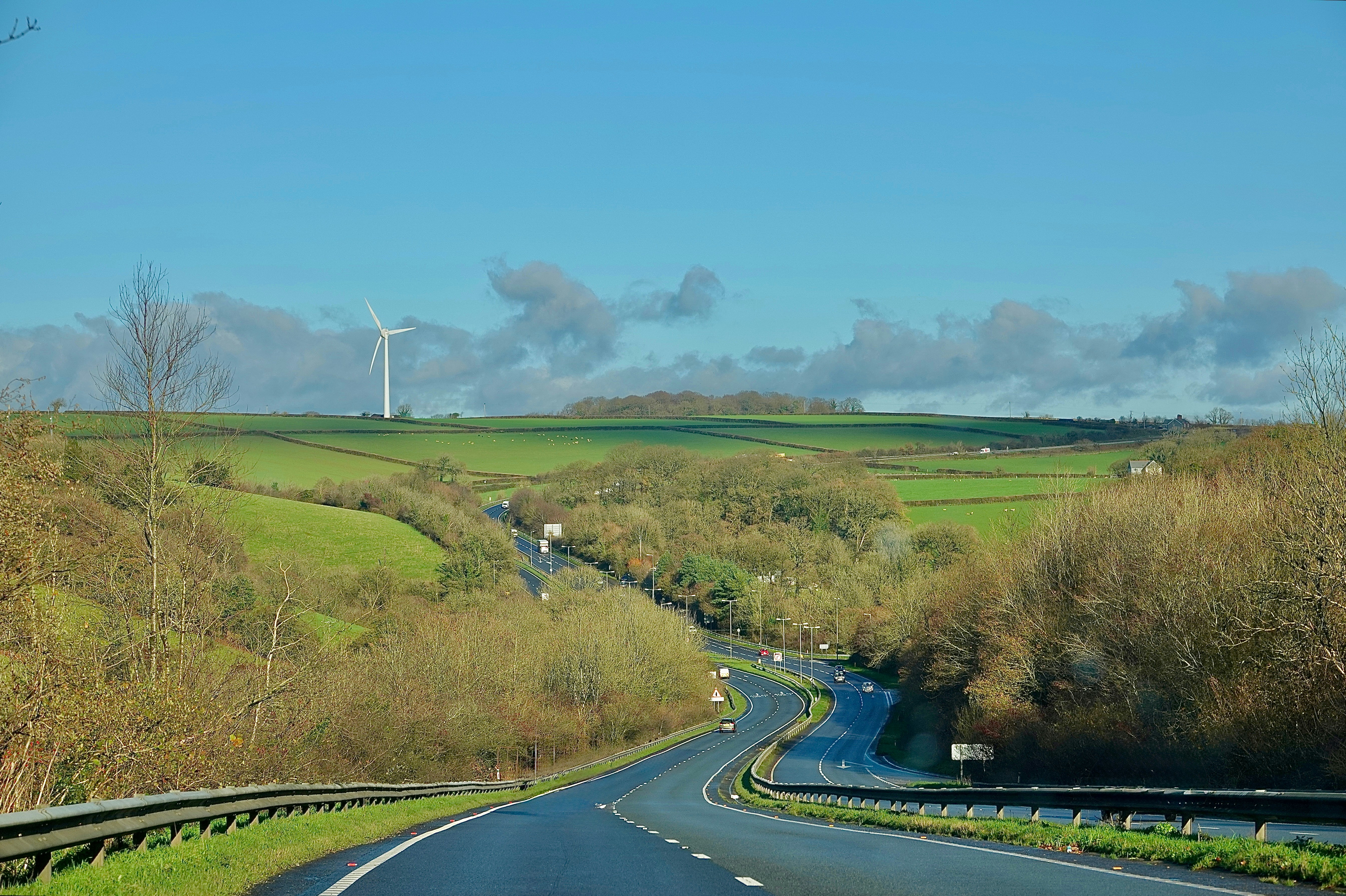 Ribbons of Road: A Quiet Descent Through Green Hills Under a Distant Wind Turbine