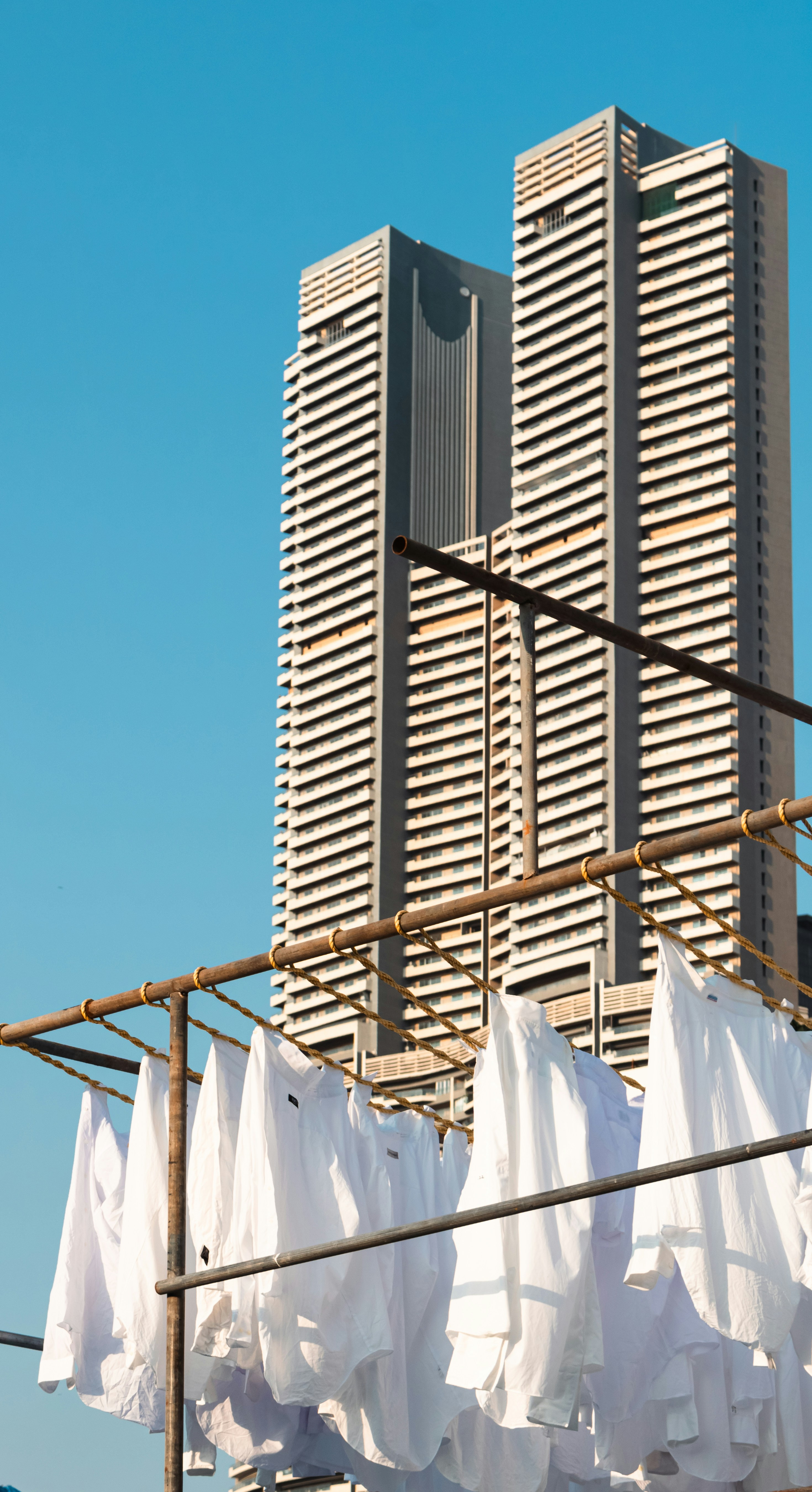 Clothes hung out to dry at Dhobi Ghat, Mumbai's iconic open-air laundromat, located near Mahalaxmi station, that is one of the world's largest of its kind. The washers, known as dhobis, work in the open to wash clothes and linens from Mumbai's hotels and hospitals. Over one lakh (100,000) clothes are washed each day. Some of the wealthier dhobis have given up on manual cleaning and have now installed large mechanical washing and drying machines. The dhobis collect clothes from all parts of the city, from Colaba to Virar. The new Minerva building can be seen in the background.