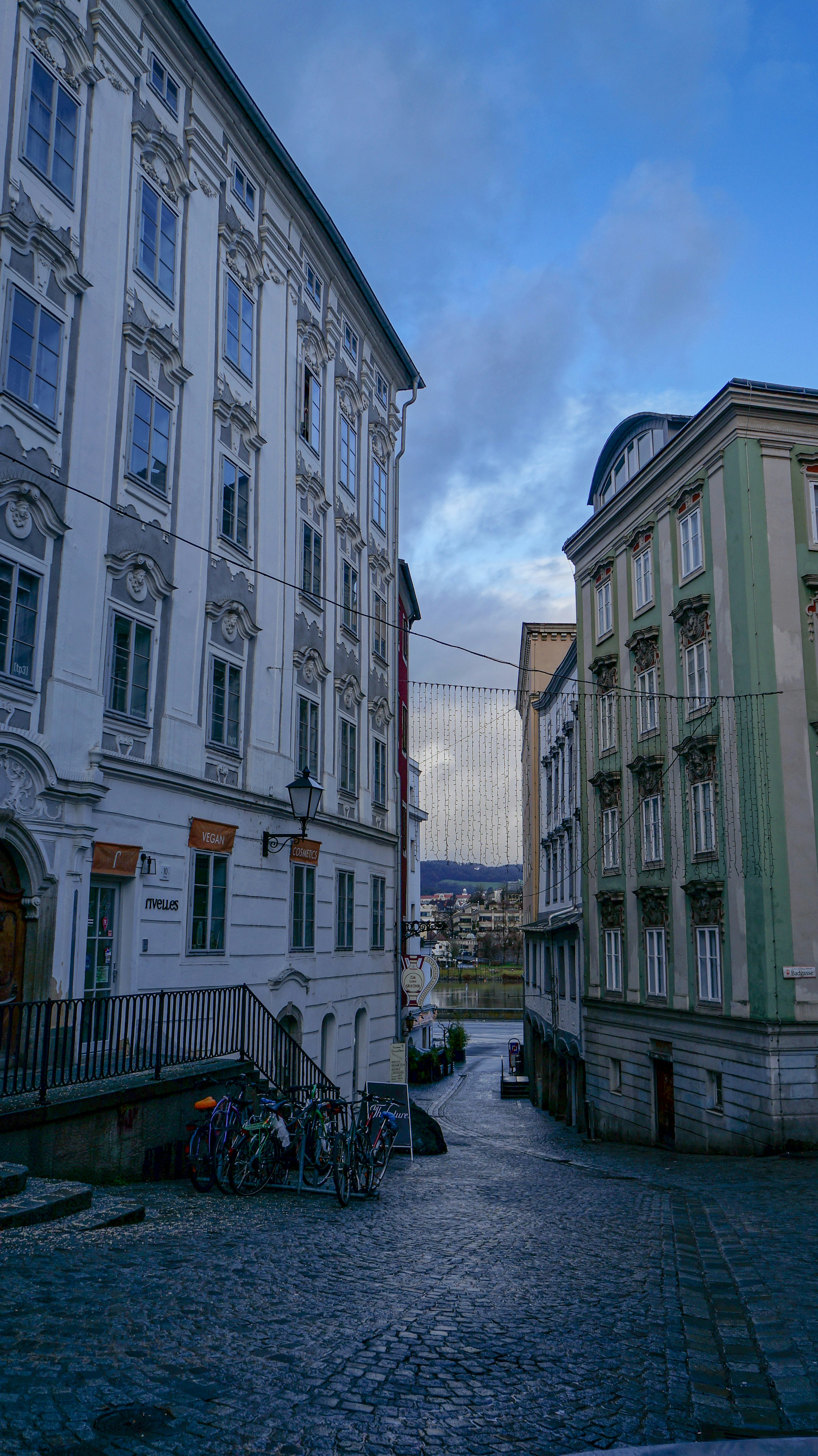 Between Facades: A Cobblestone Street Toward a Distant River