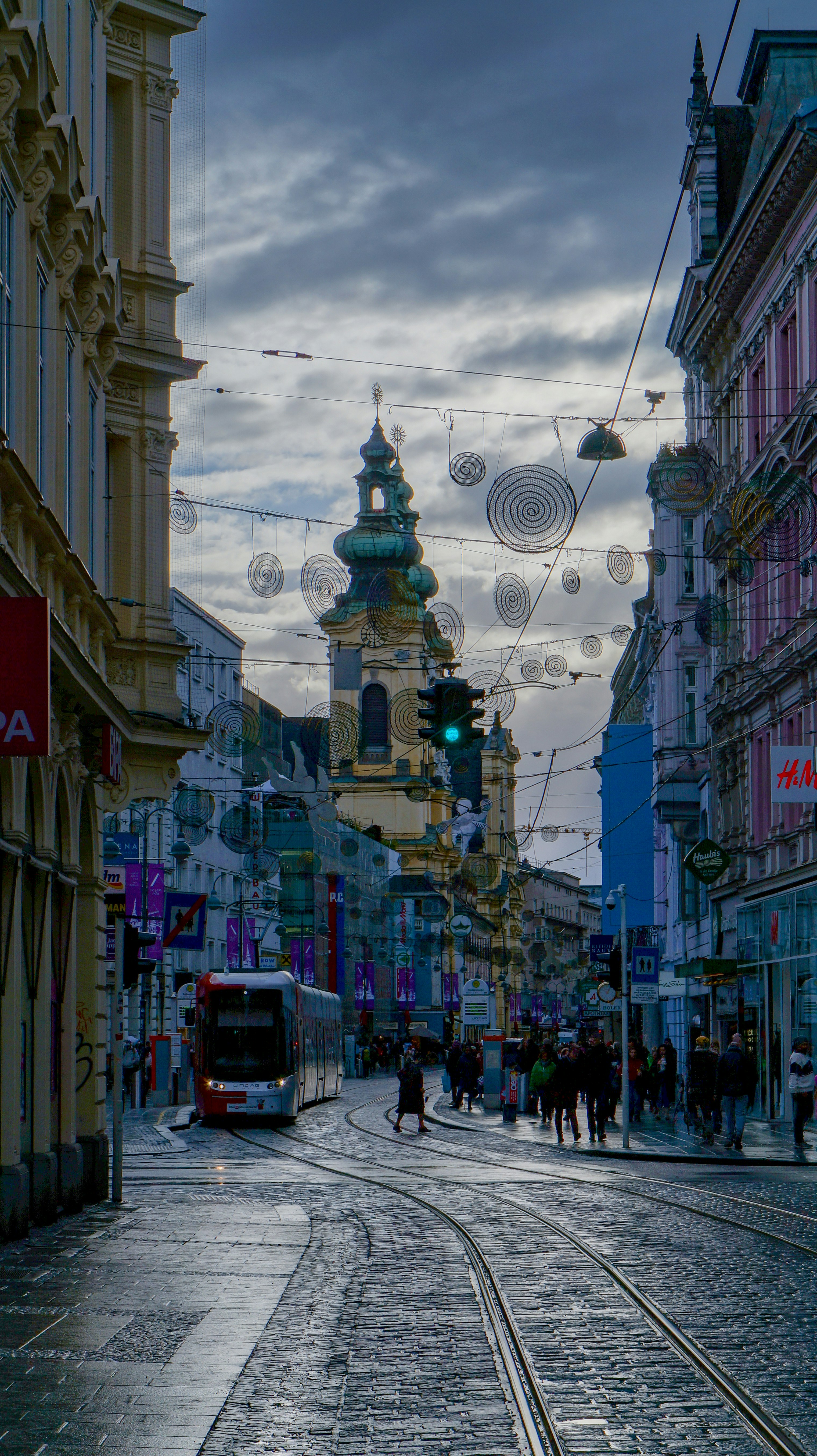 Street with tram tracks and historic buildings under cloudy sky.