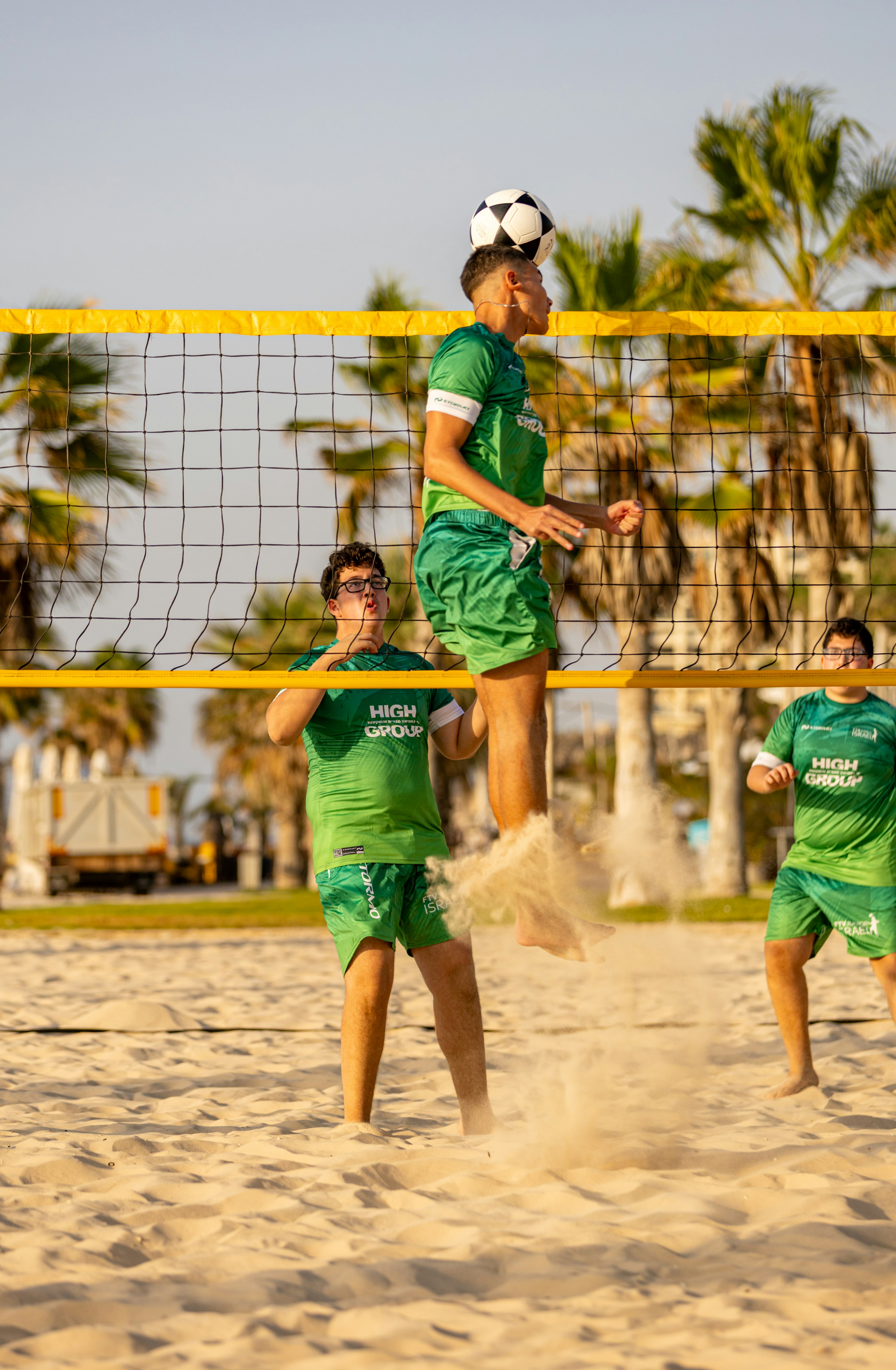 Young man balancing soccer ball on head on beach.